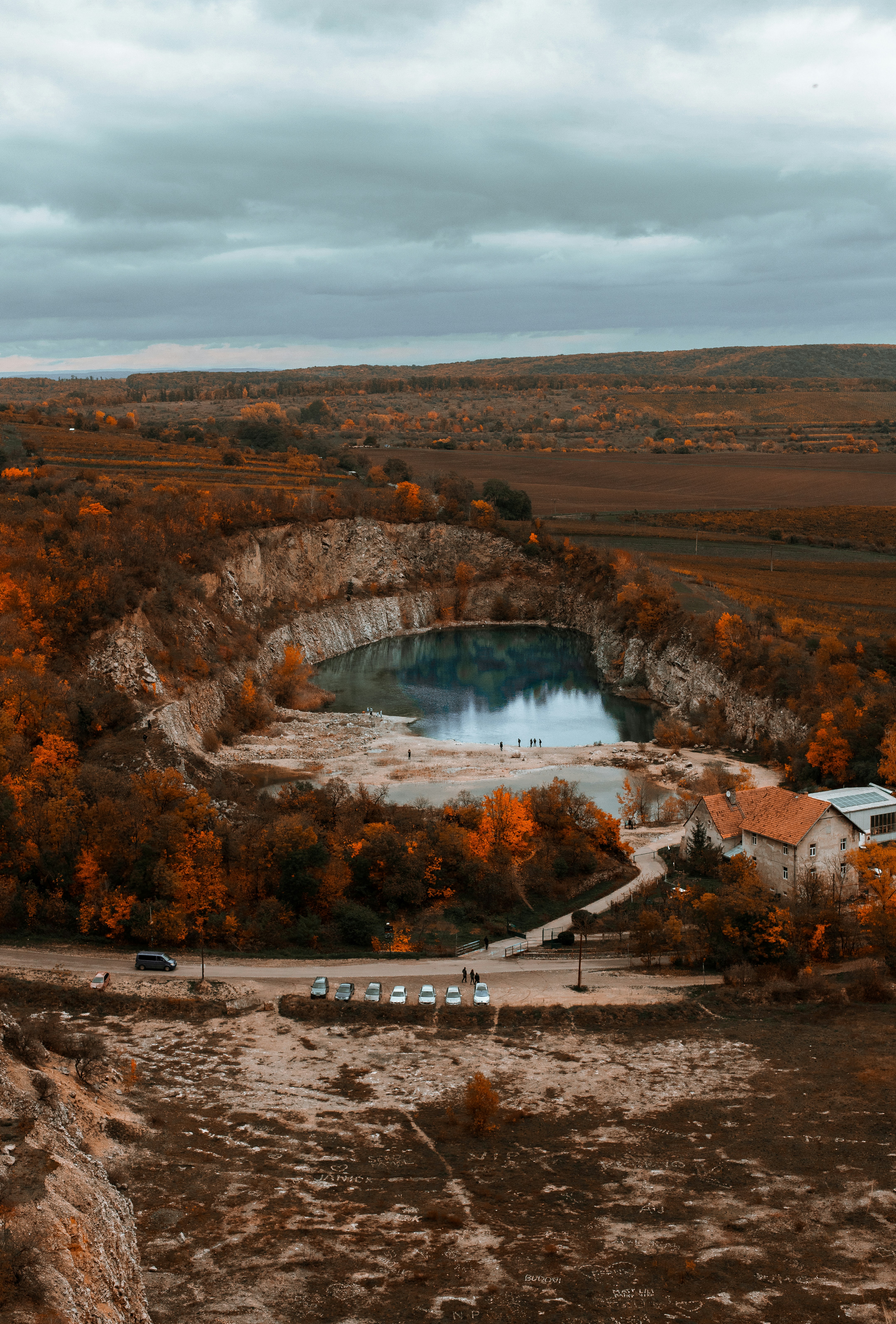 Serene quarry lake encircled by autumn foliage under a cloudy sky.