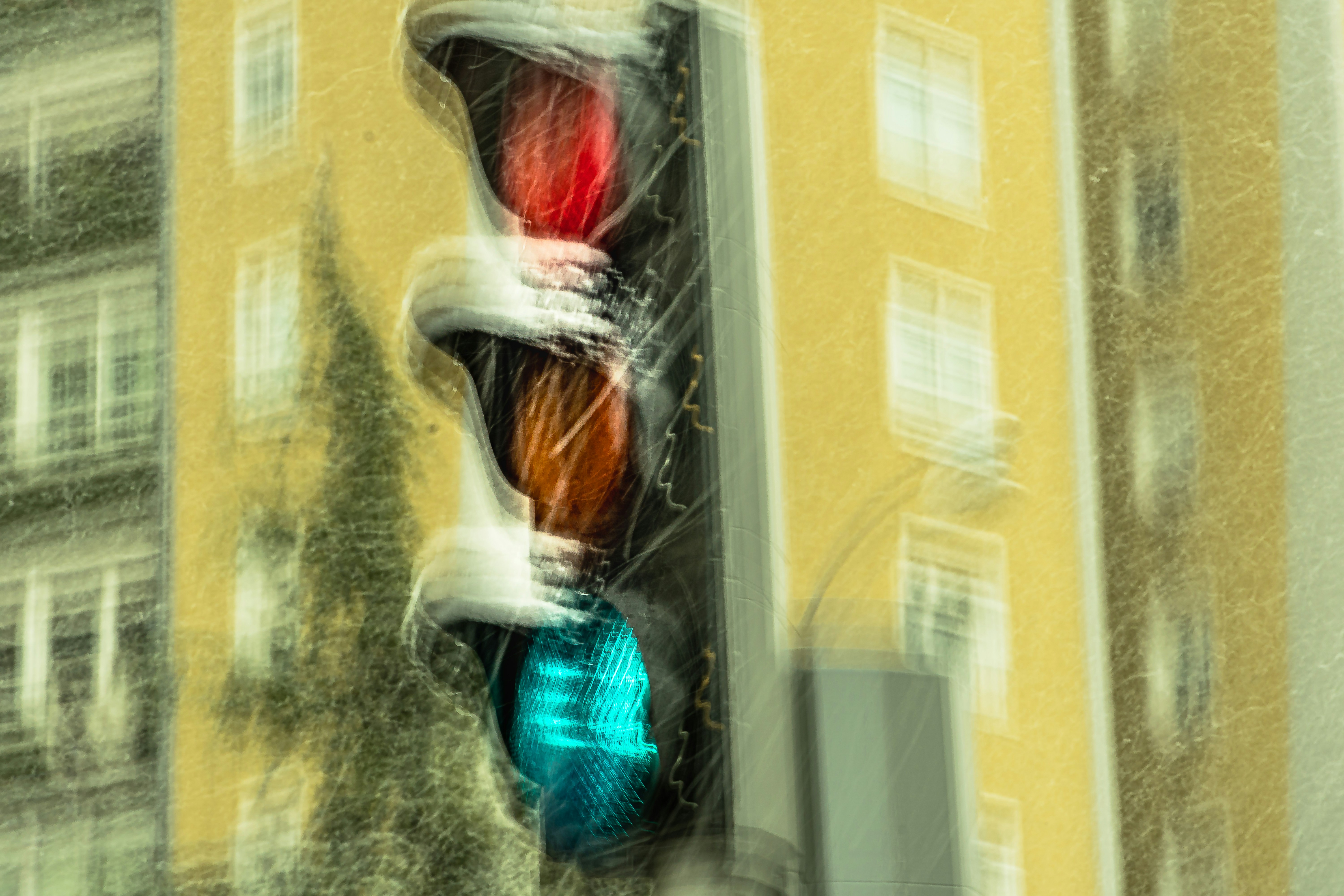 Traffic light displaying red, yellow, and green signals amidst a blurred urban backdrop, capturing the essence of a bustling city in the rain.