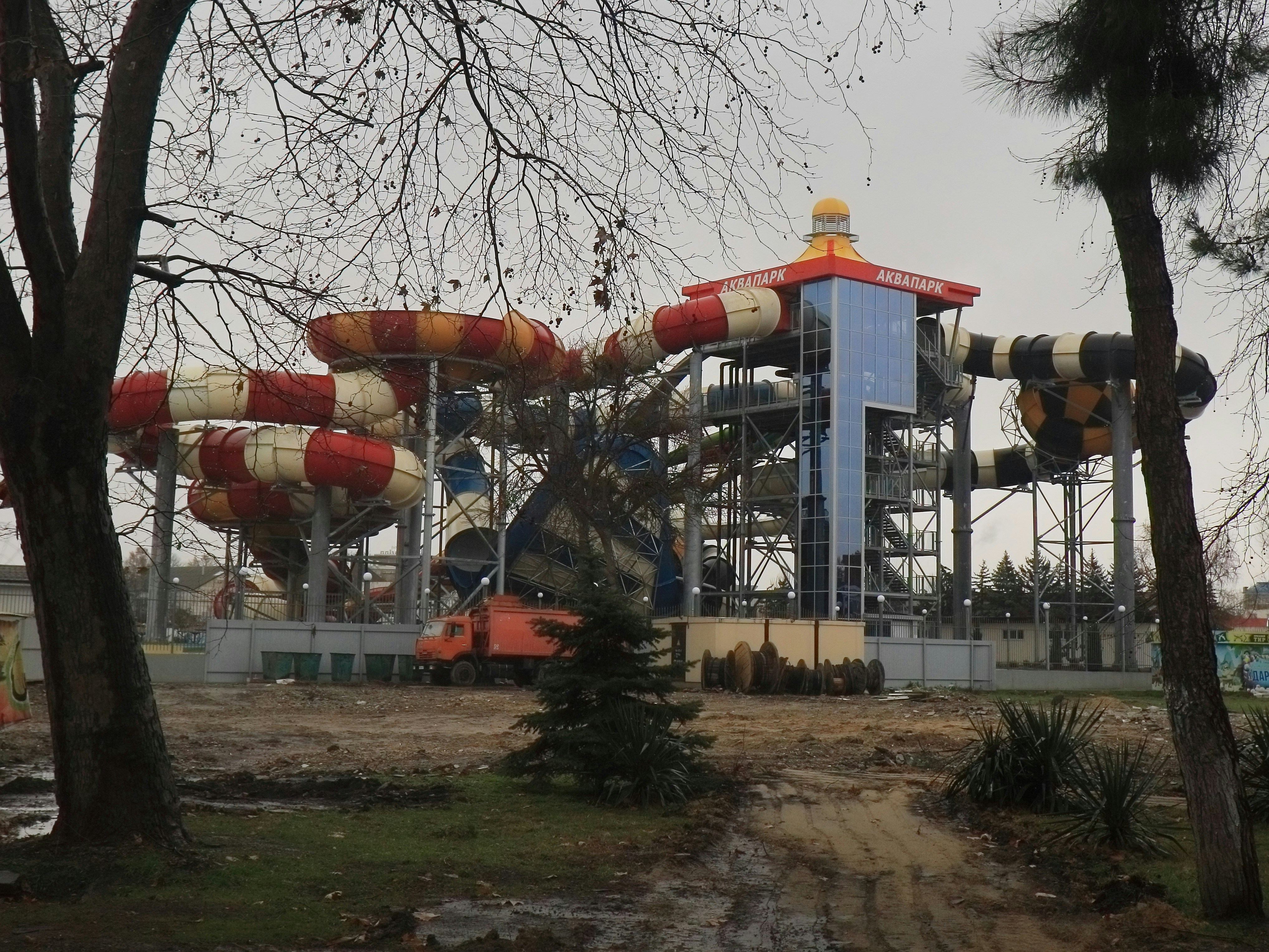 Colorful water slides tower over a muddy landscape, hinting at a vibrant water park experience. The structure is framed by trees, creating a contrast between nature and man-made excitement.