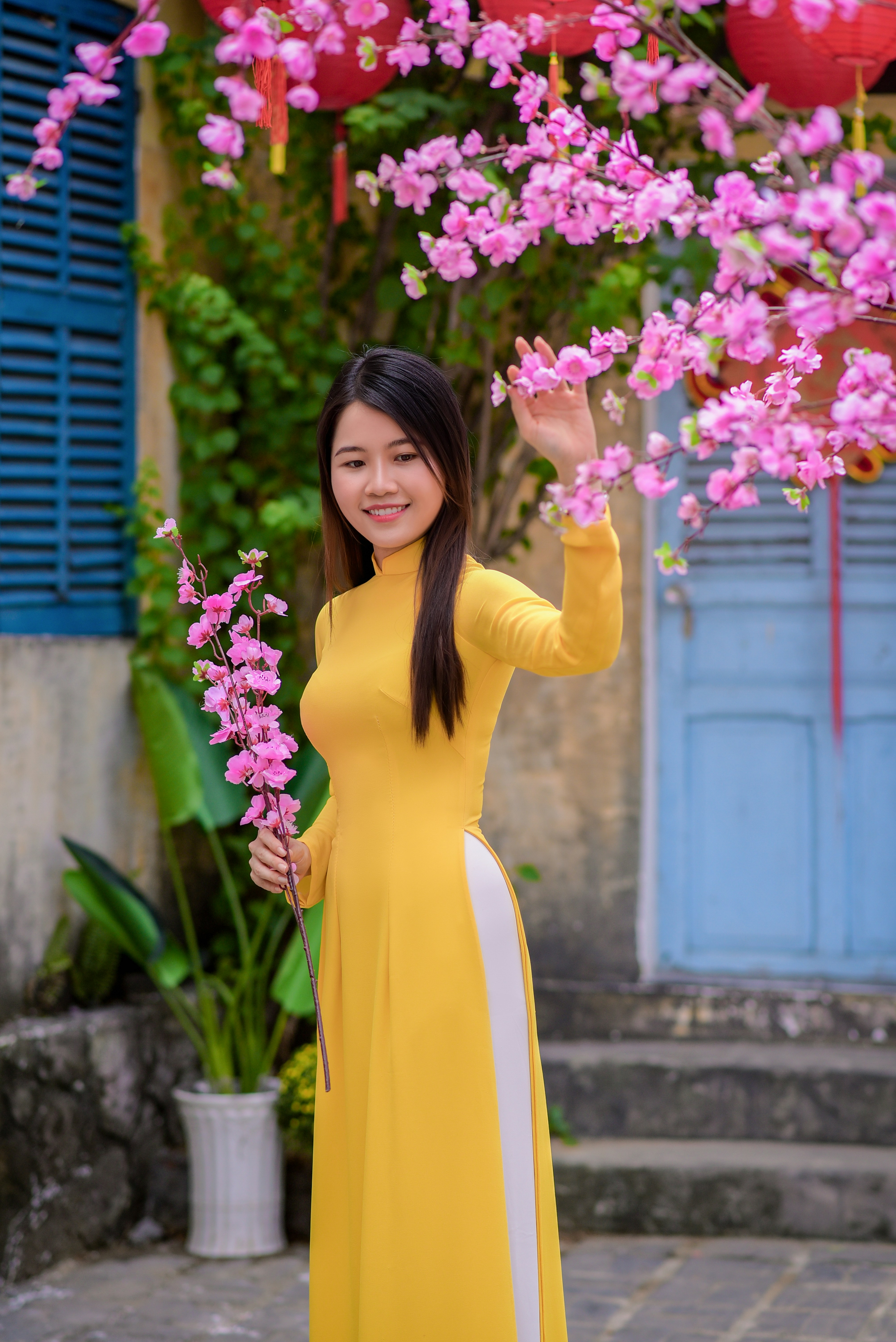 Yellow Ao Dai Amid Pink Blossom Arches by a Weathered Blue Door
