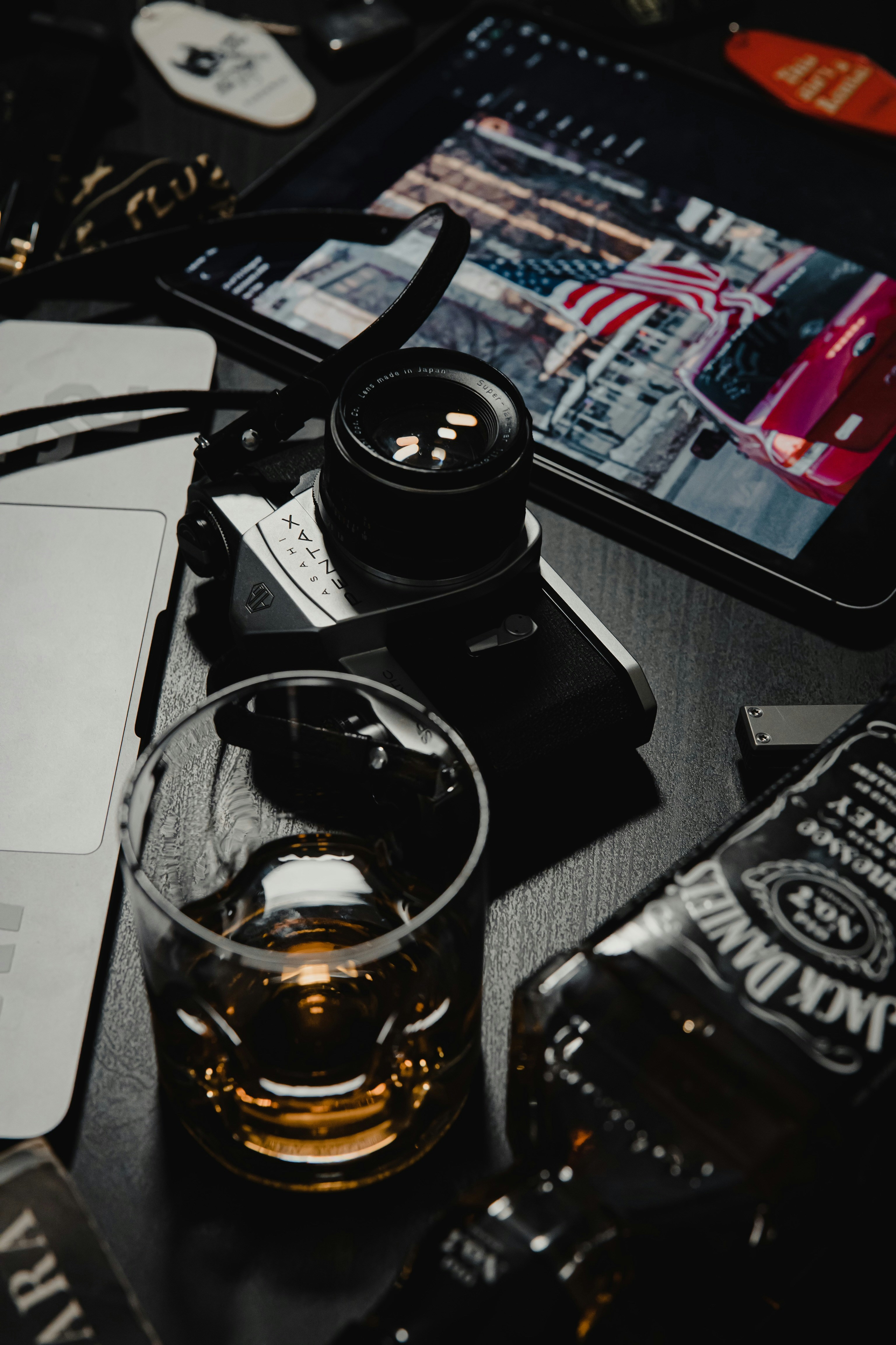 Close-Quarters Lens: A Vintage Camera, Whiskey, and Screens on a Dim Desk