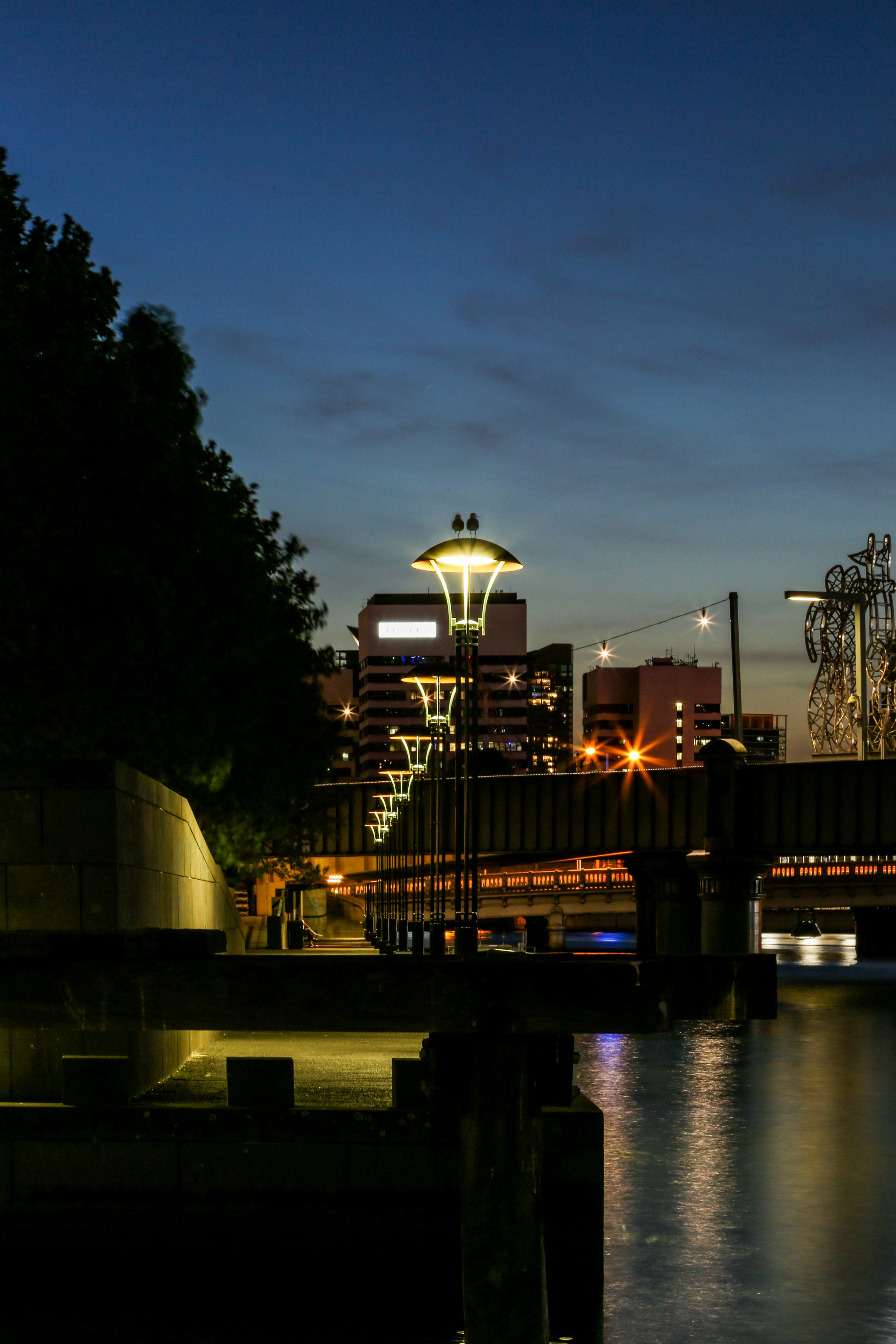 Lamplight Corridor Along a Quiet Riverside at Blue Hour