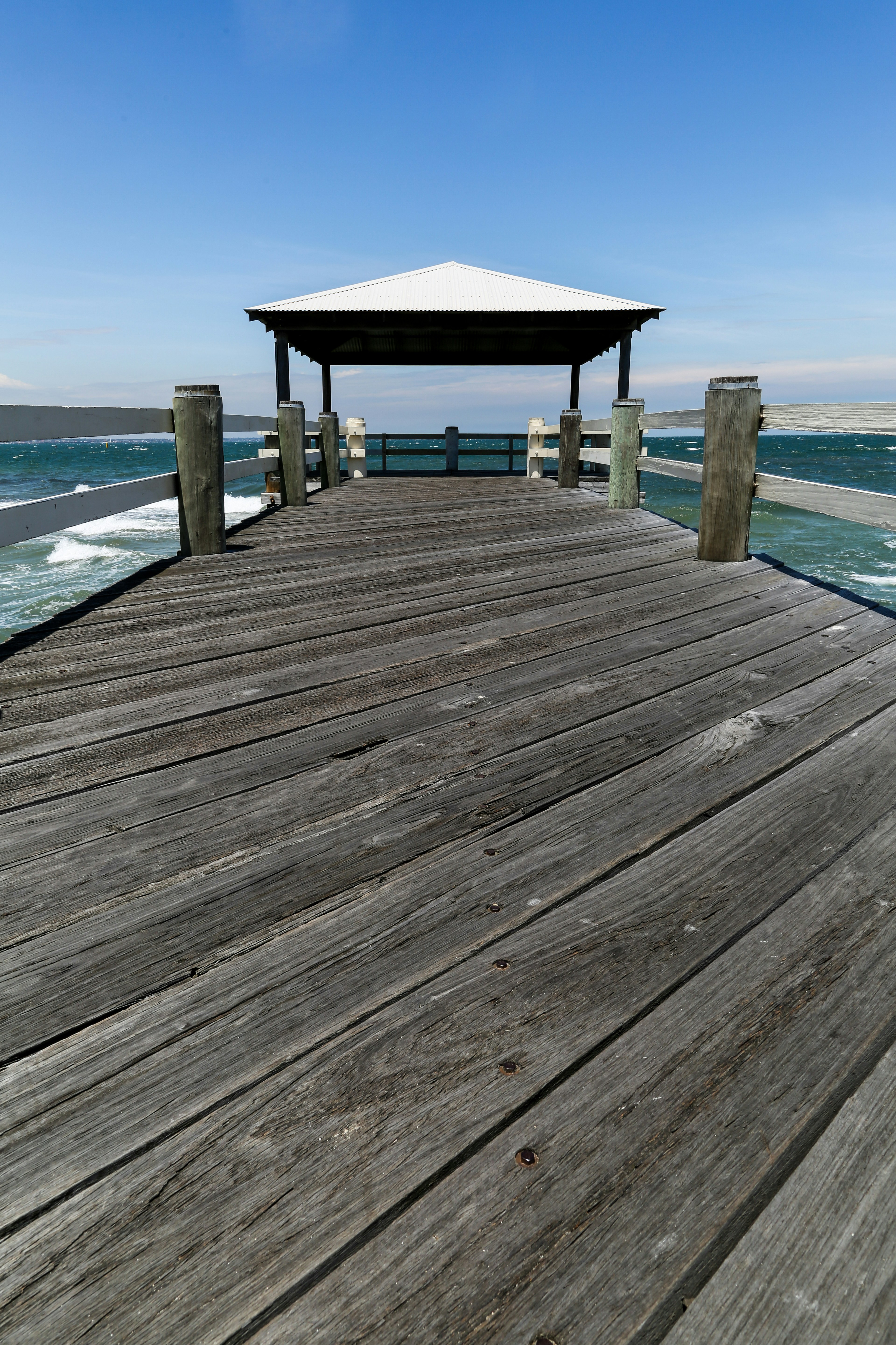 Toward the Gazebo: Weathered Pier Reaching the Sea Under a Clear Sky