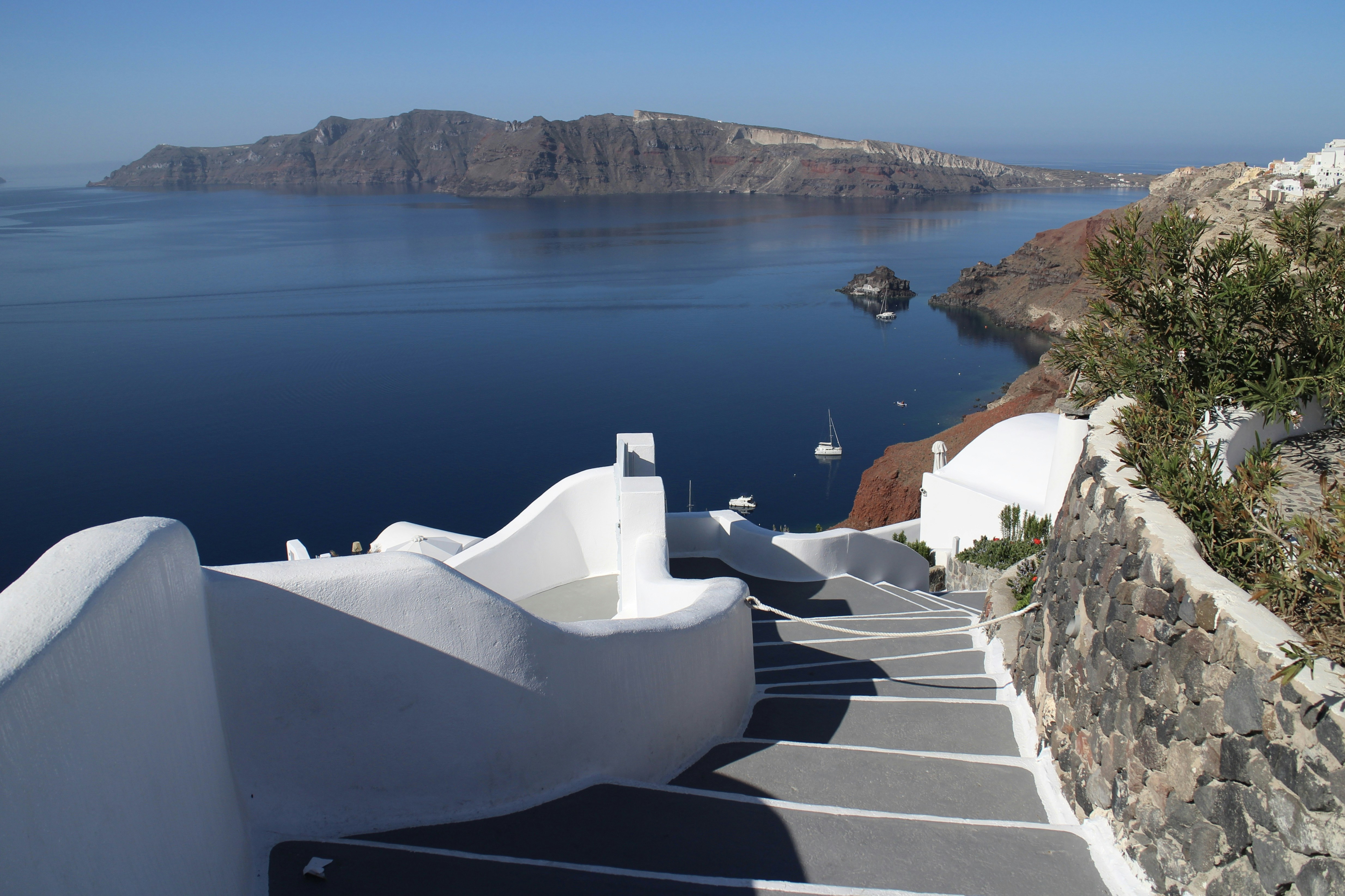 White stone steps leading down a hillside with a view of calm blue sea and distant islands under a clear sky.