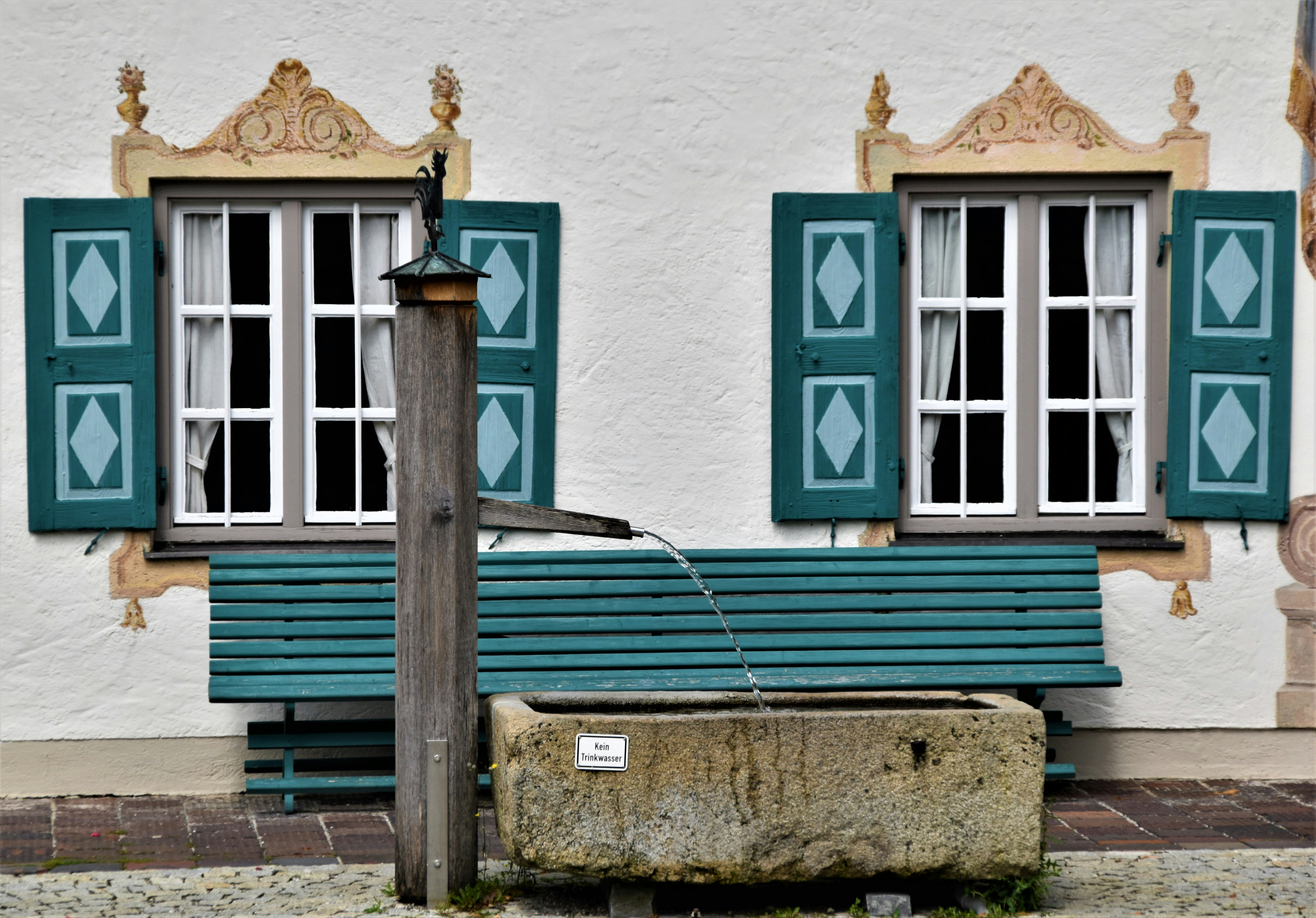 Water Arc Over a Weathered Fountain Before Teal-Shuttered Windows