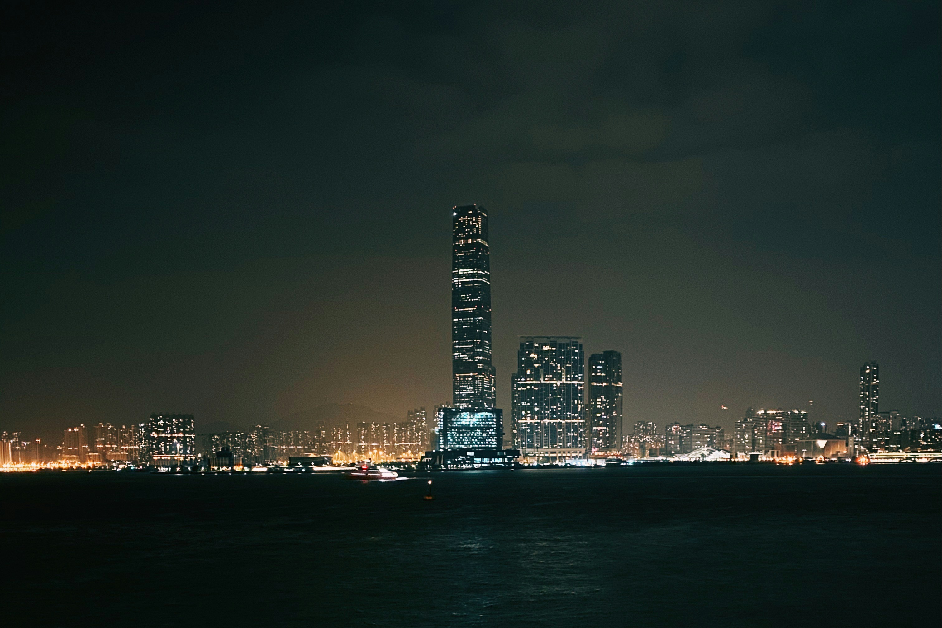 Illuminated skyscrapers reflect on the water's surface, showcasing a vibrant cityscape at night. The contrast between the dark sky and glowing buildings creates a striking visual narrative.