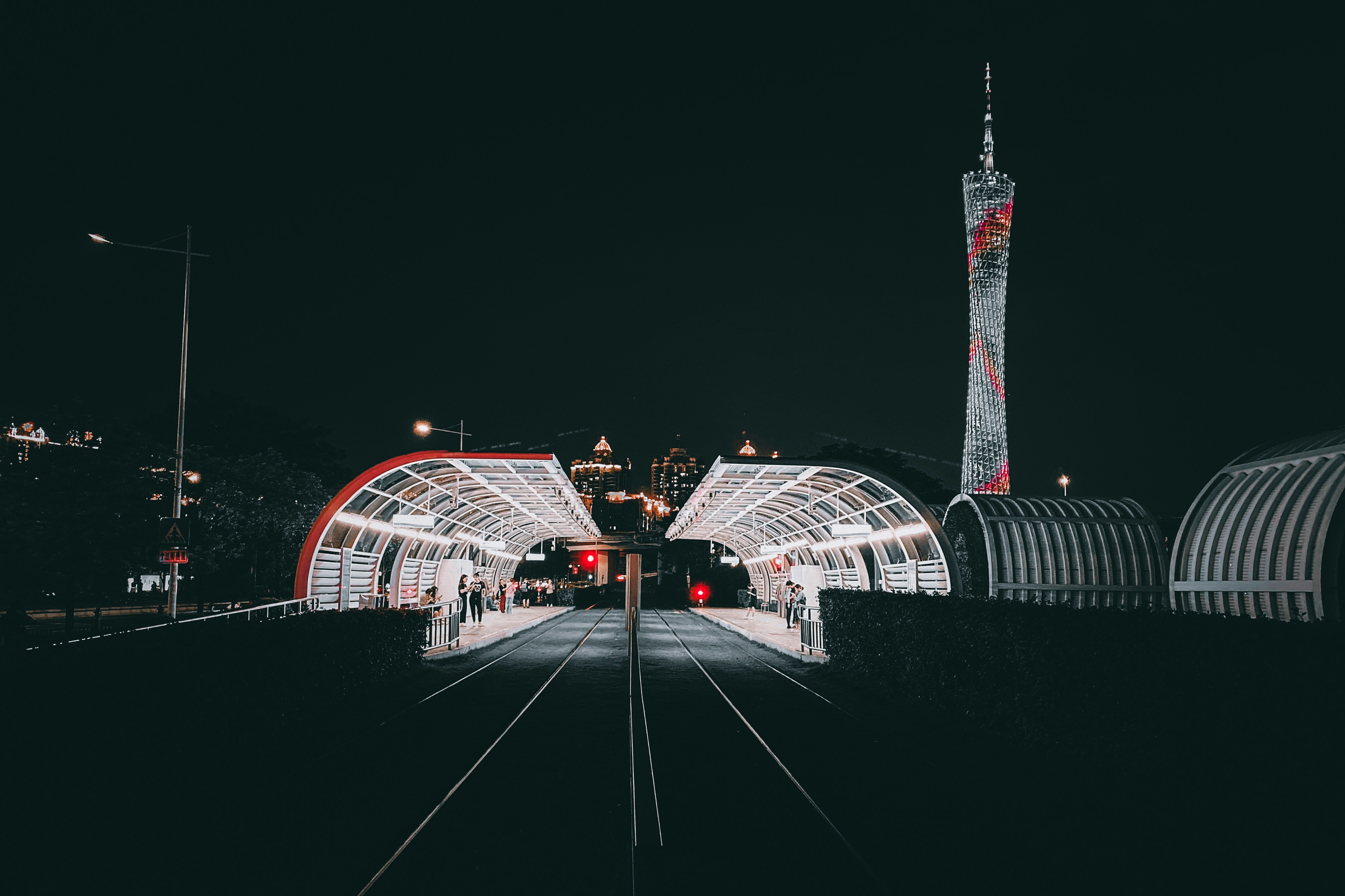 Illuminated transit station with sleek architecture and a towering landmark in the background at night.