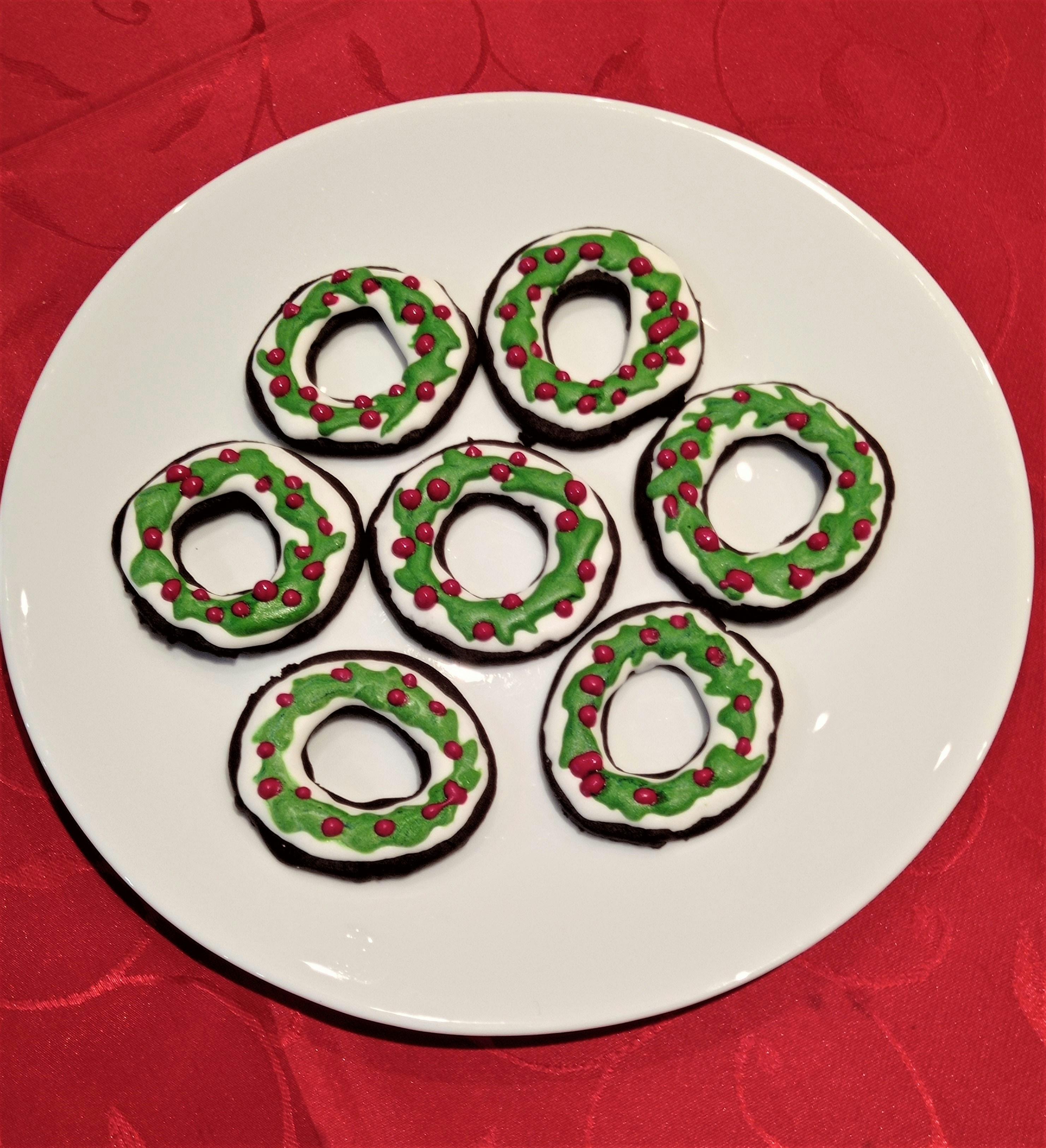 A plate of decorated wreath-shaped cookies featuring green icing and red accents, arranged neatly for a festive presentation.