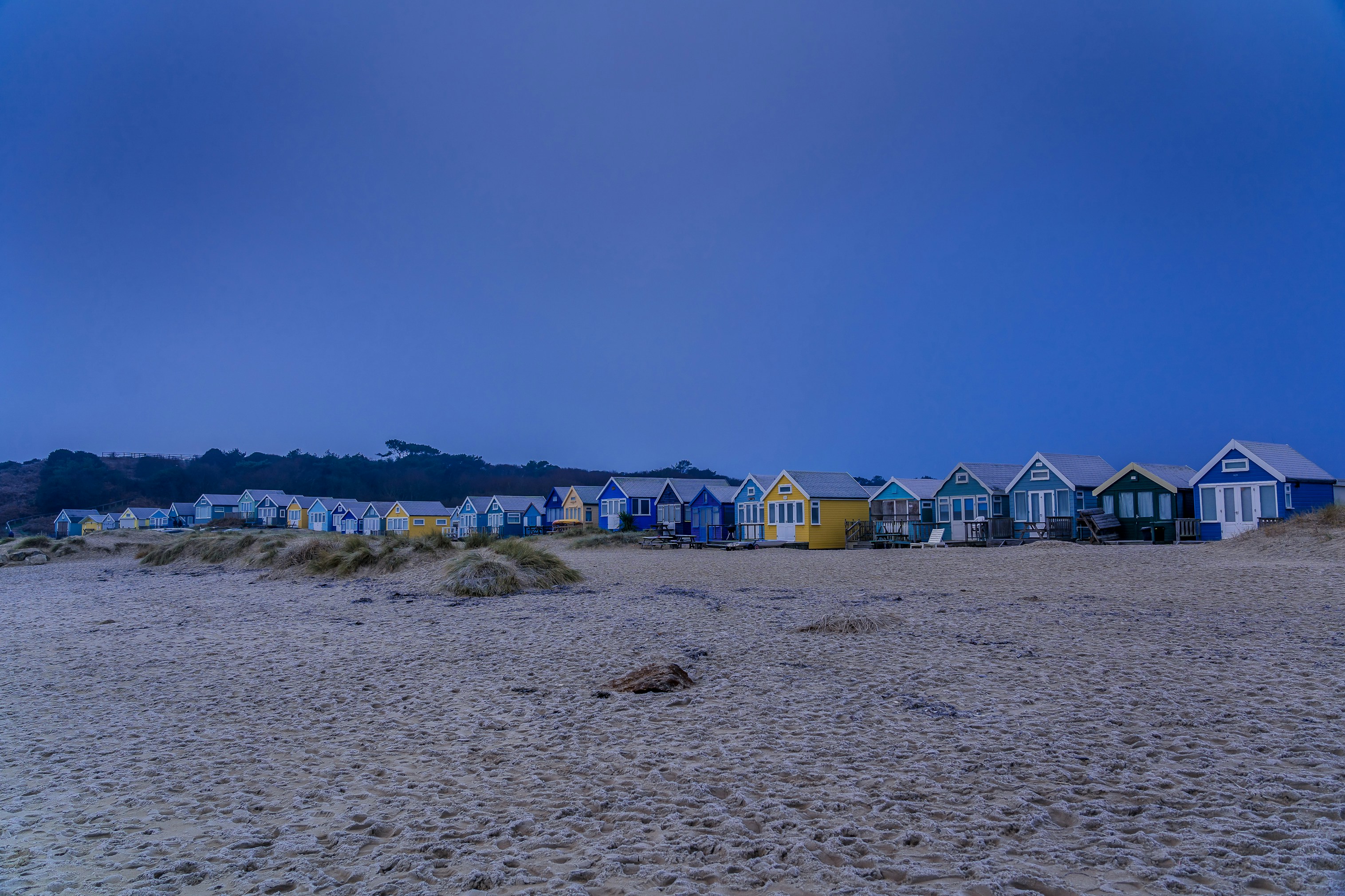 Pastel Row on the Dunes: Beach Huts Under a Broad Blue Sky