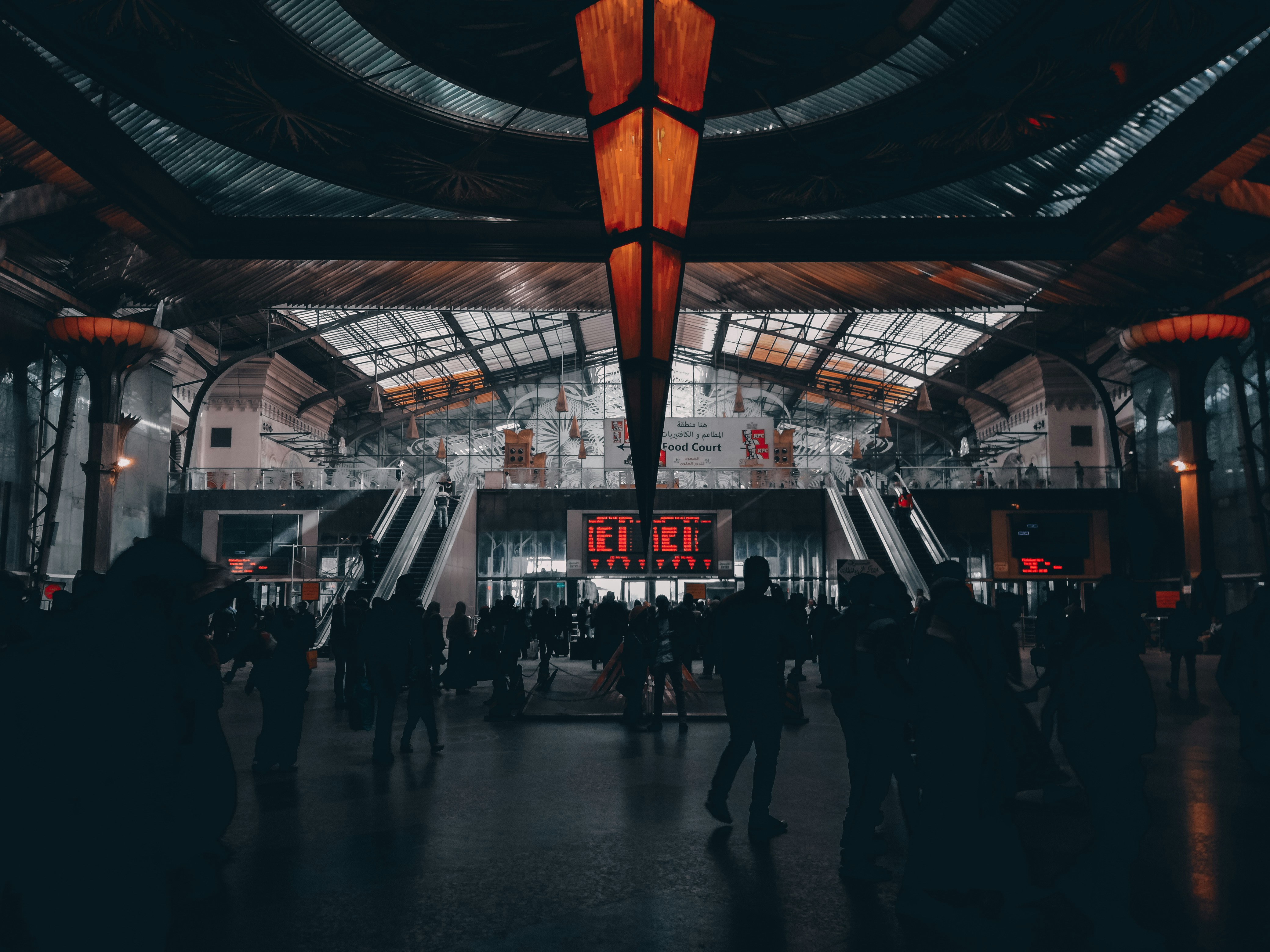 Silhouetted commuters in a dimly lit train station with escalators and a large digital clock.