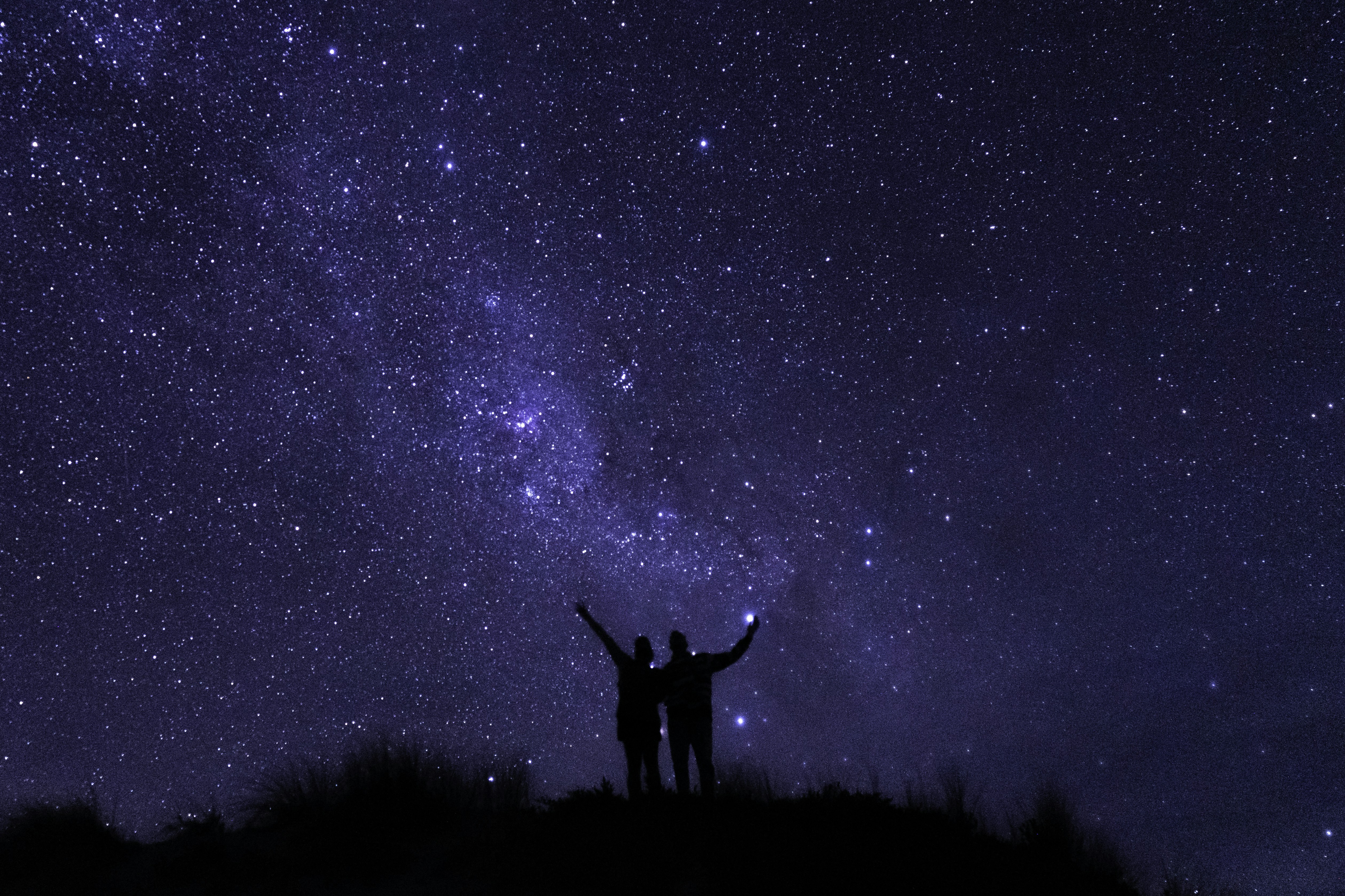 Silhouetted figures raise arms beneath a vast starry night sky.