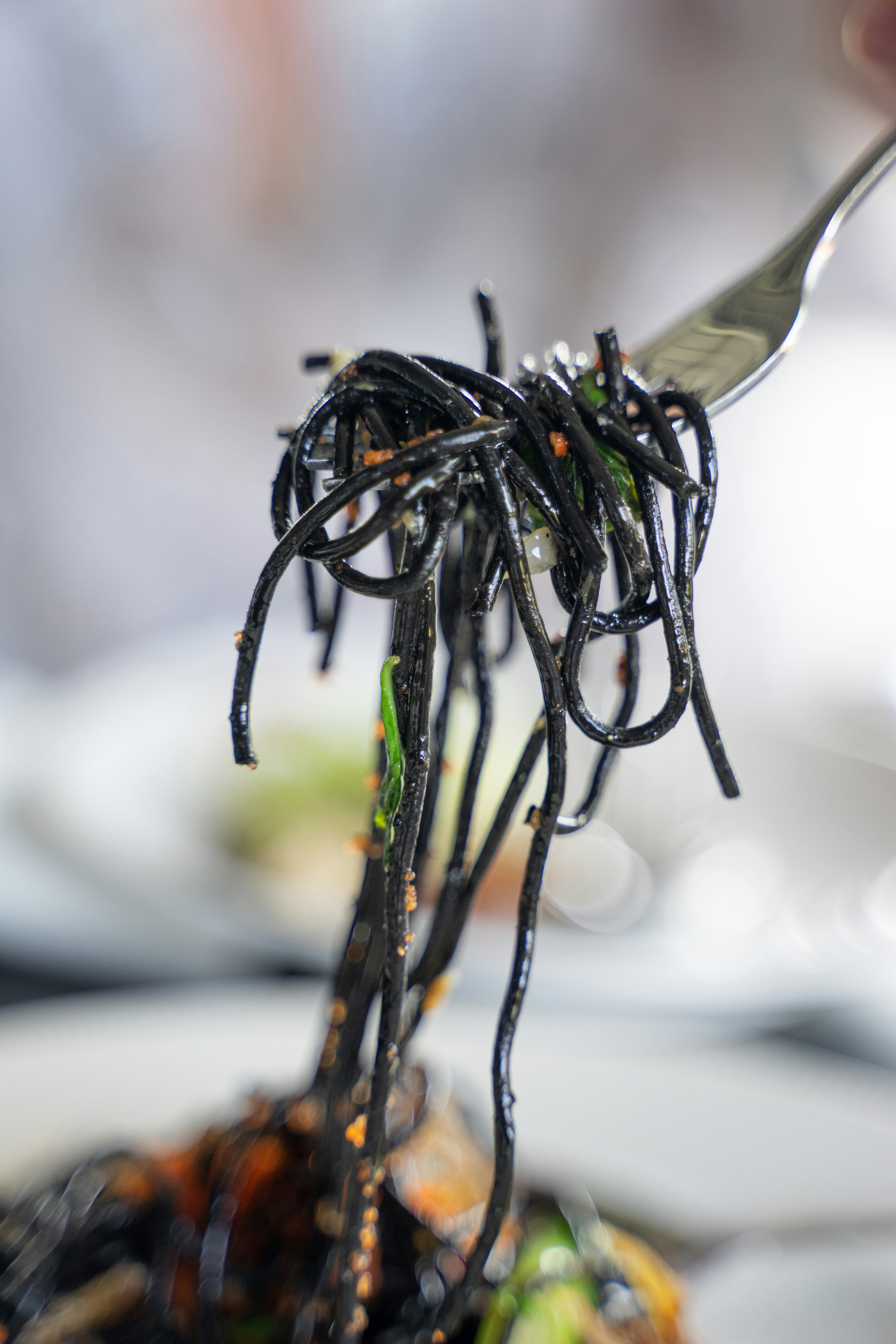 Squid-ink spaghetti on a fork: glossy, tangled threads under soft restaurant light