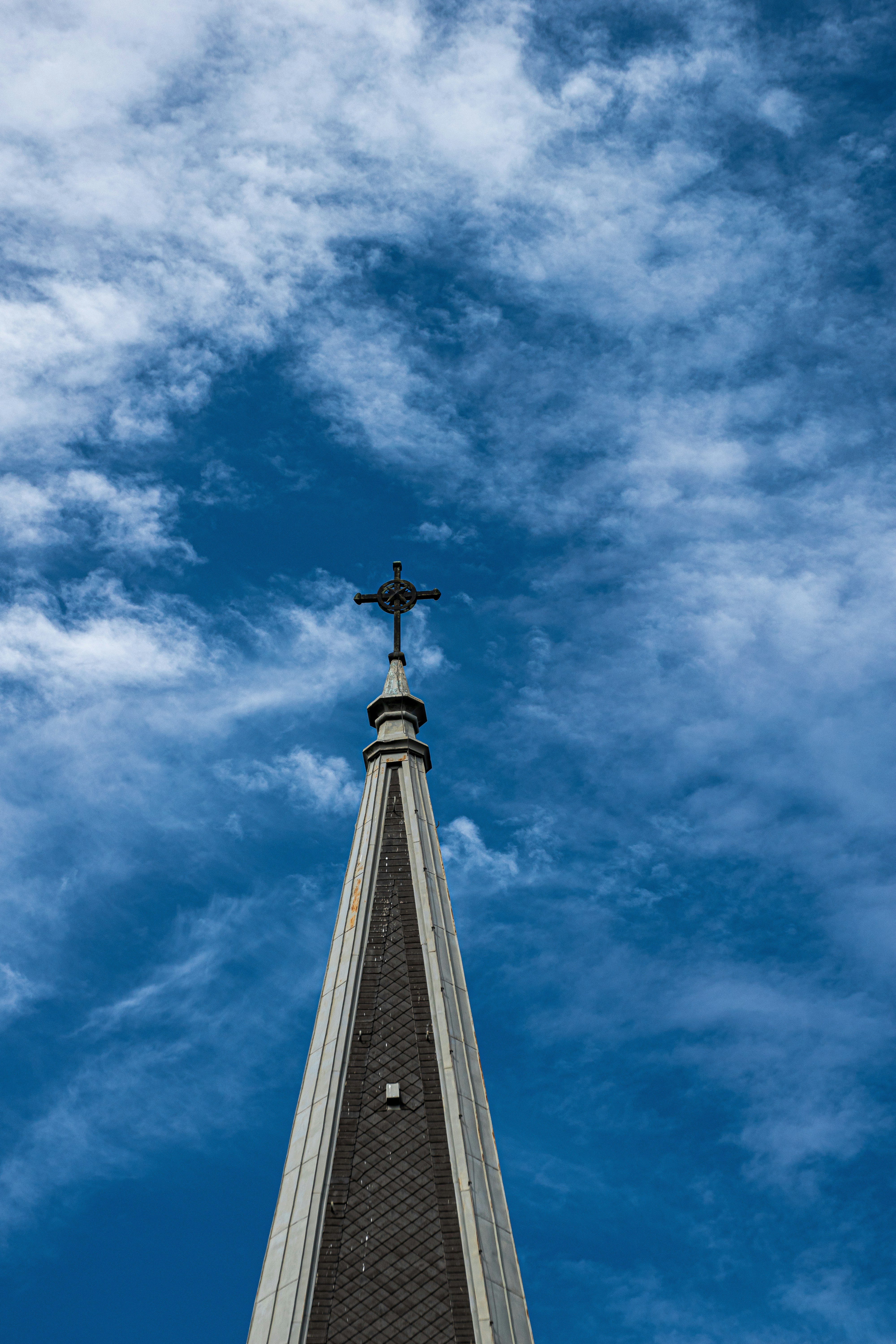 black cross on top of gray concrete tower under blue and white cloudy sky during daytime