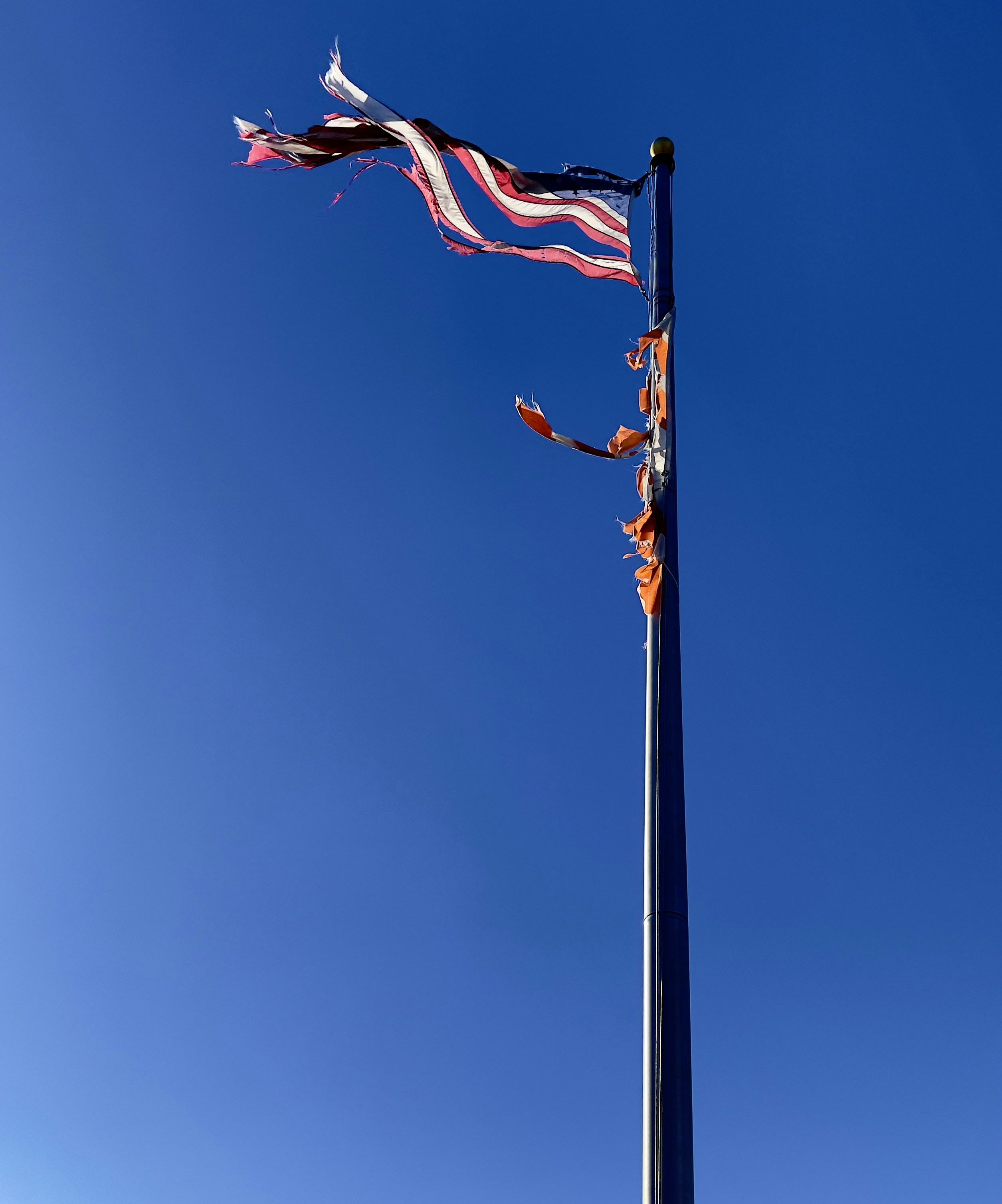 Frayed flag fluttering against a clear blue sky, symbolizing resilience and history.