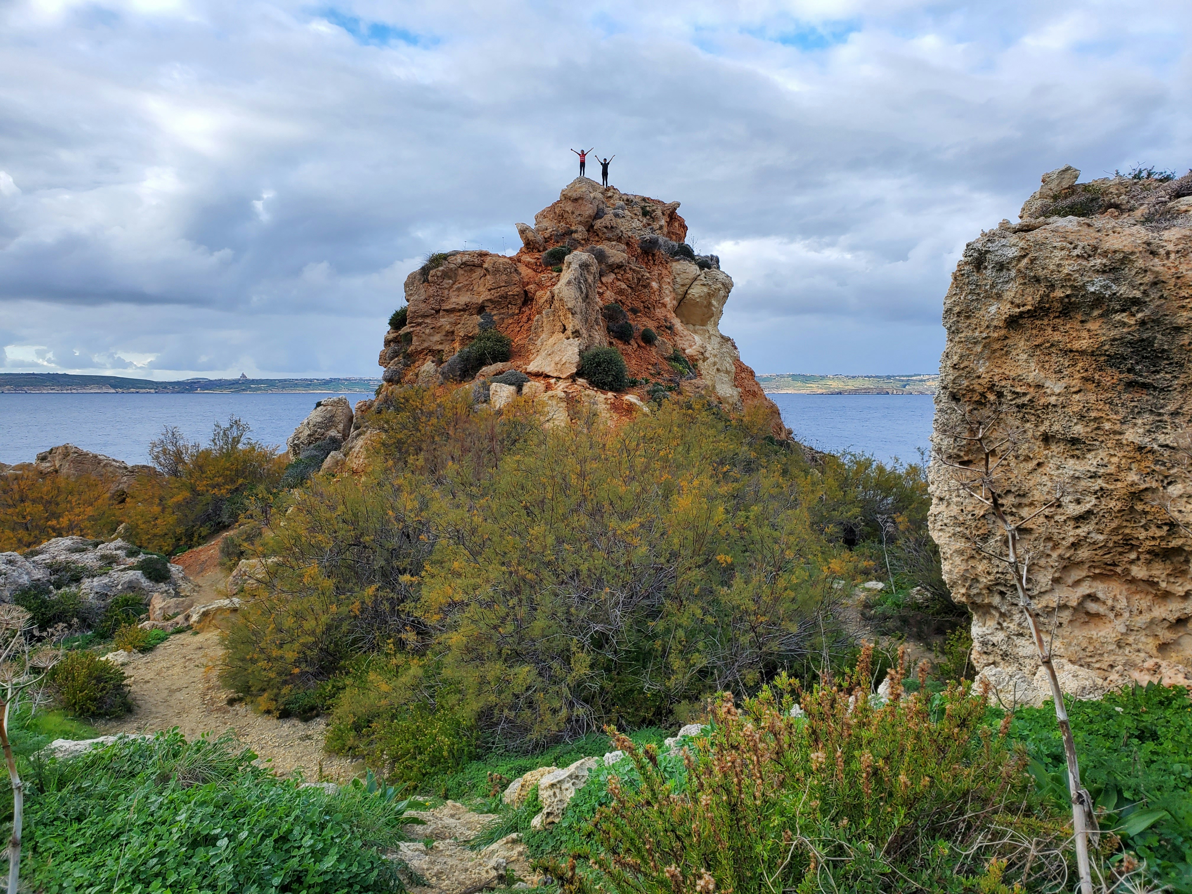 Rock Sentinel: Human Figures atop a Weathered Pinnacle Overlooking a Coastal Basin