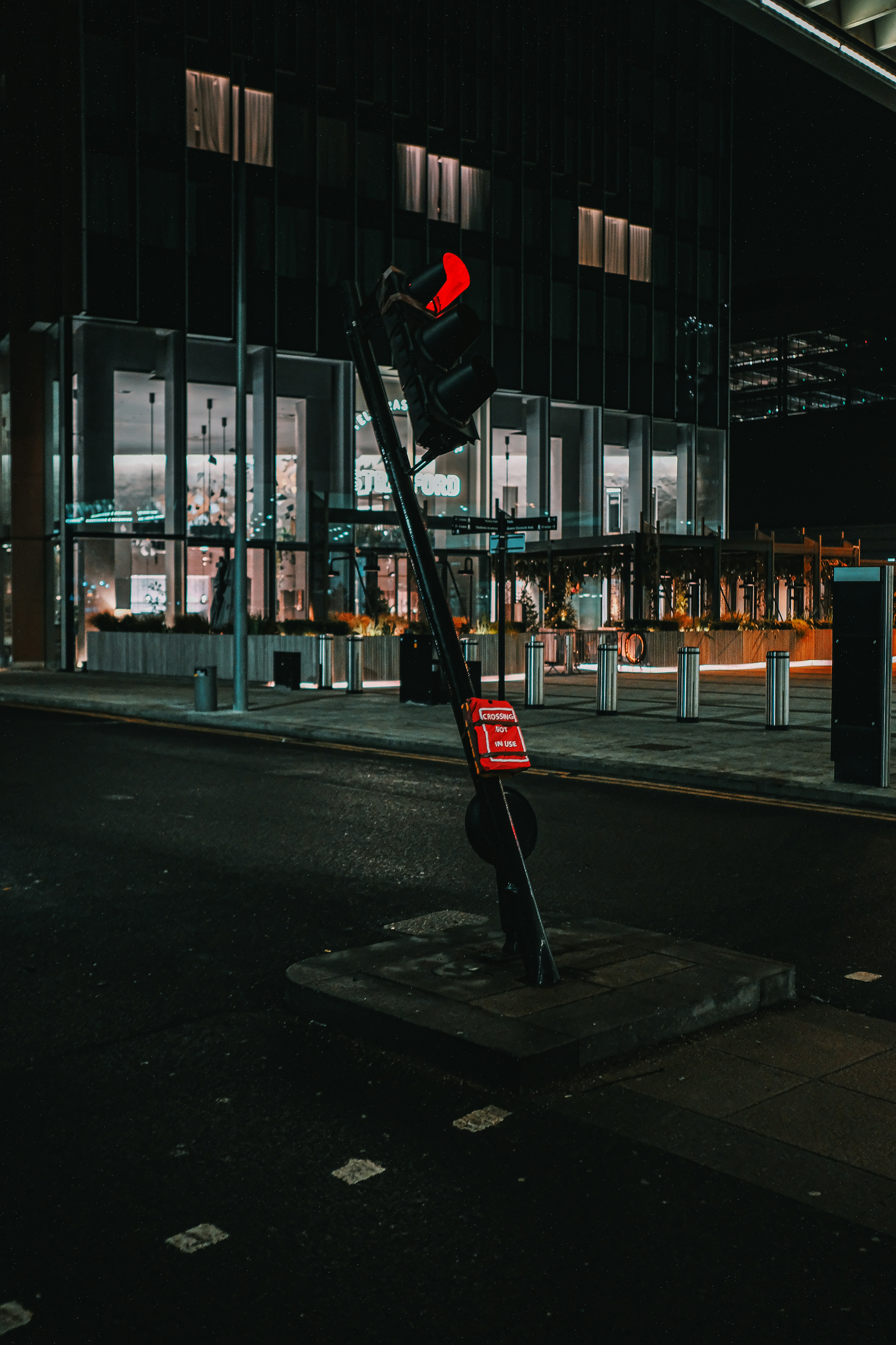 A traffic light with a red signal stands prominently against a modern urban backdrop at night, highlighting the stillness of the city. The scene captures the interplay of artificial light and architecture.