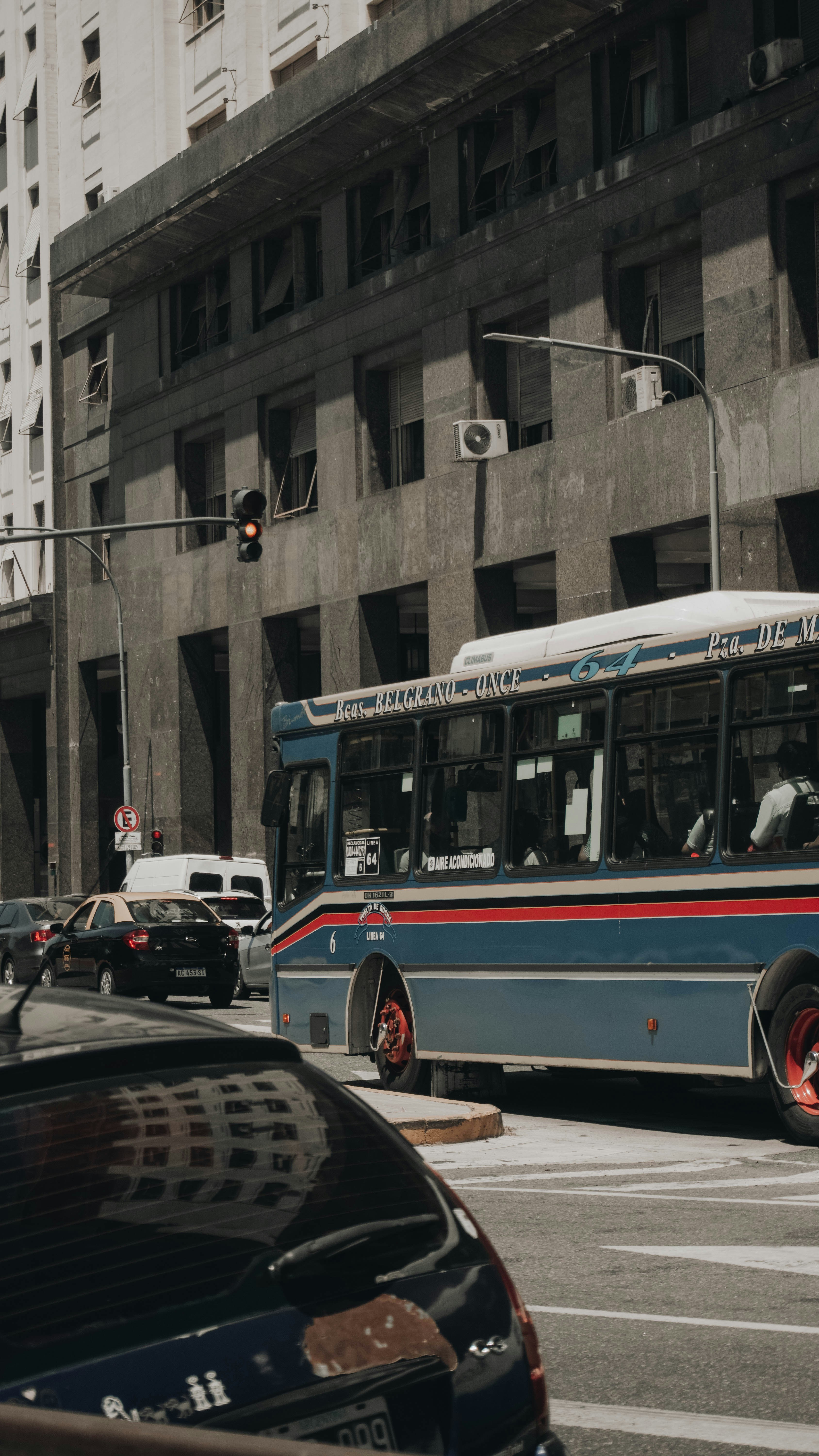 A blue and white city bus navigates through a busy intersection, surrounded by cars and urban architecture. The scene captures the dynamic nature of city transportation.