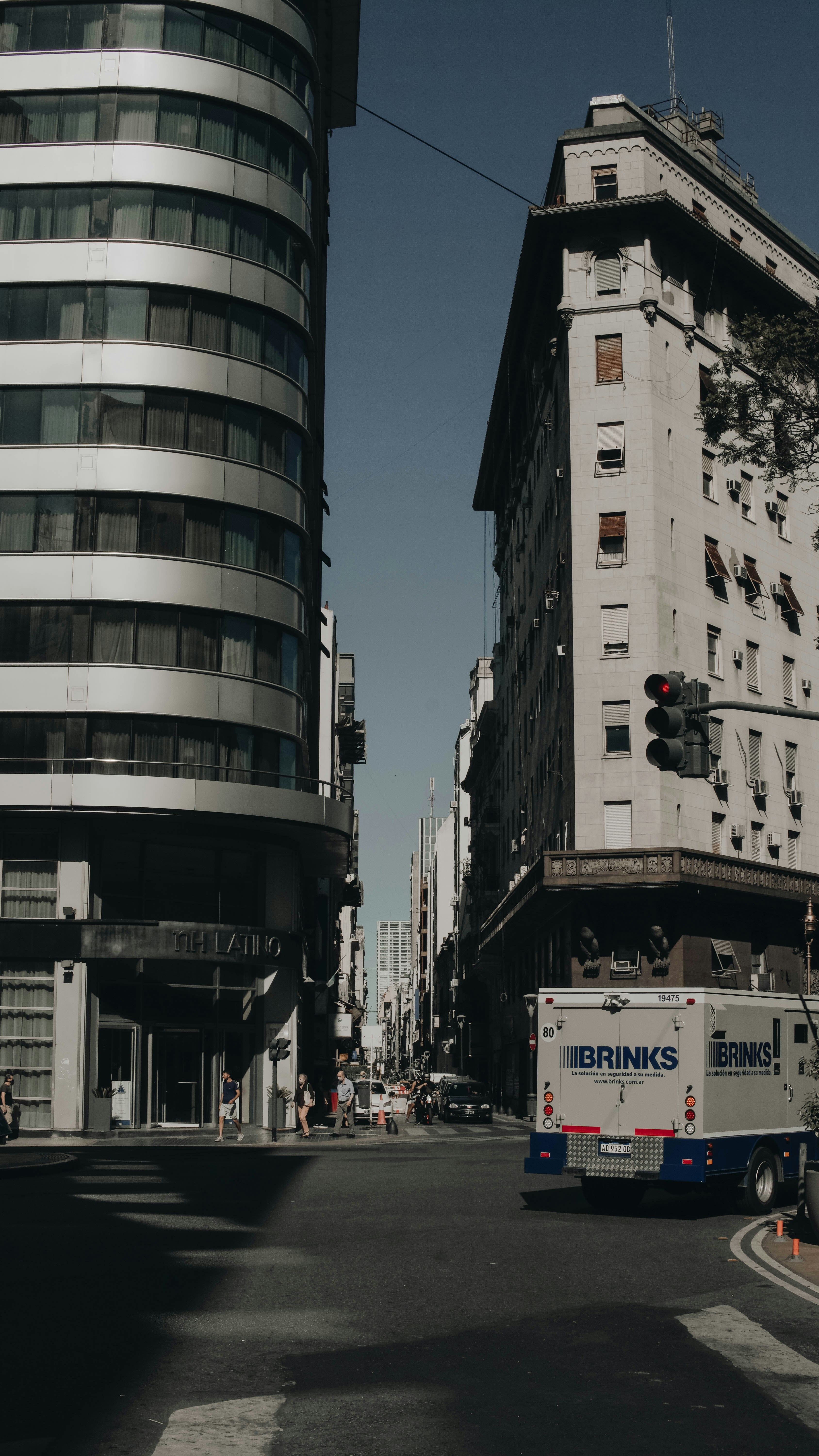 A BRINKS armored truck navigating a city intersection, framed by modern and historic architecture under a clear sky.