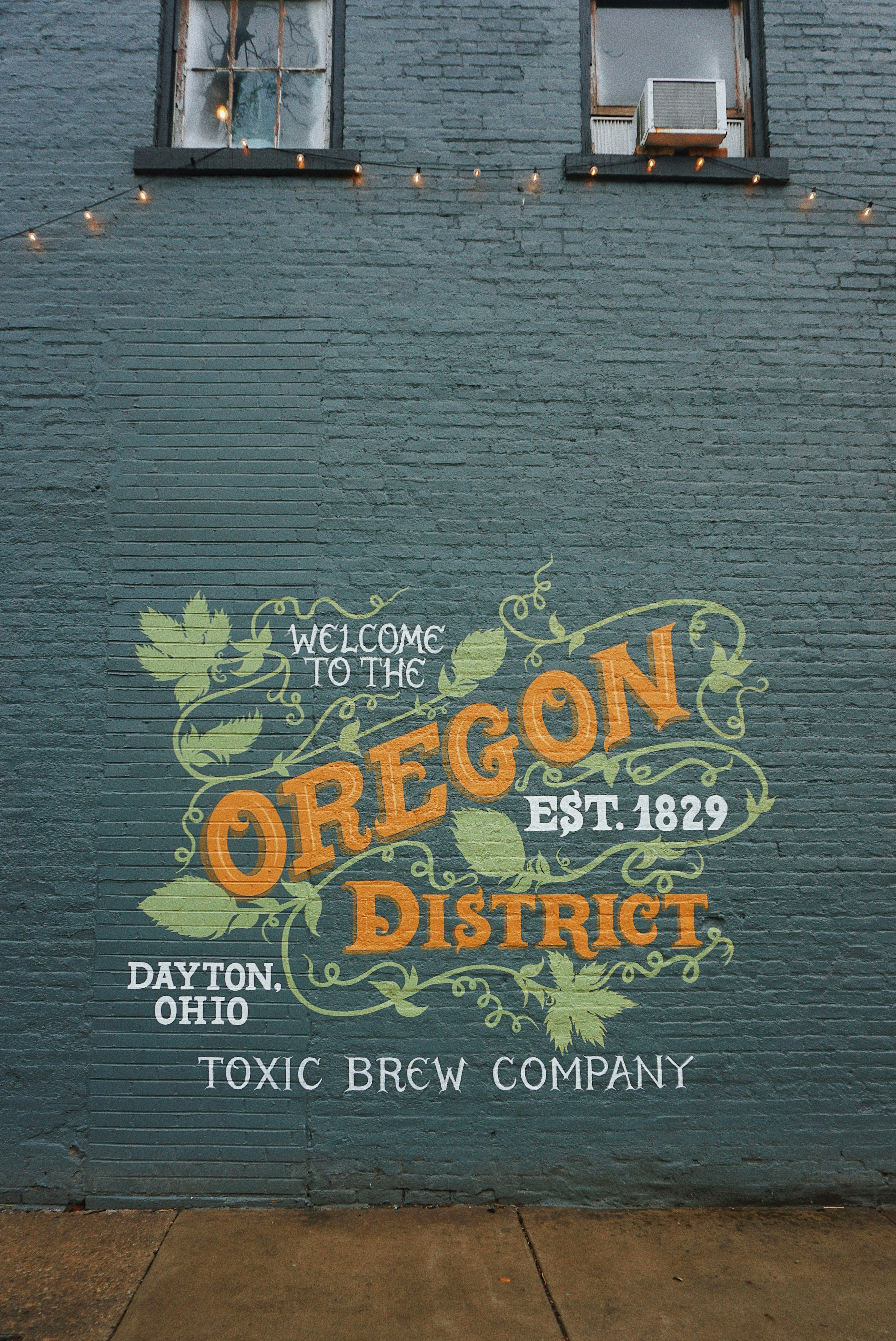 Mural on a brick wall depicting a welcome message for the Oregon District with vintage typography.