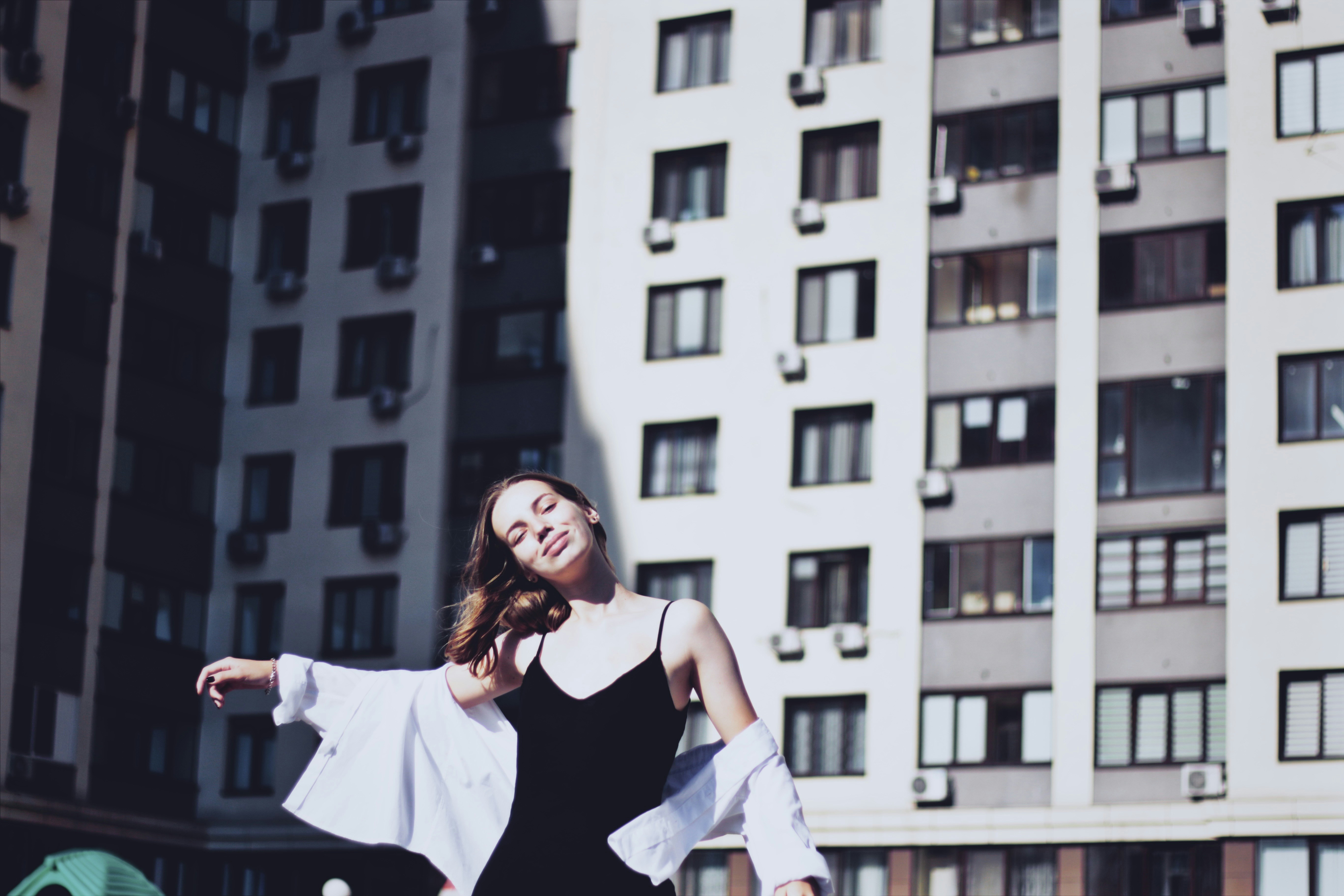 Young woman in a black outfit playfully twirls with a white shirt in an urban setting, showcasing a stylish blend of fashion and city life.