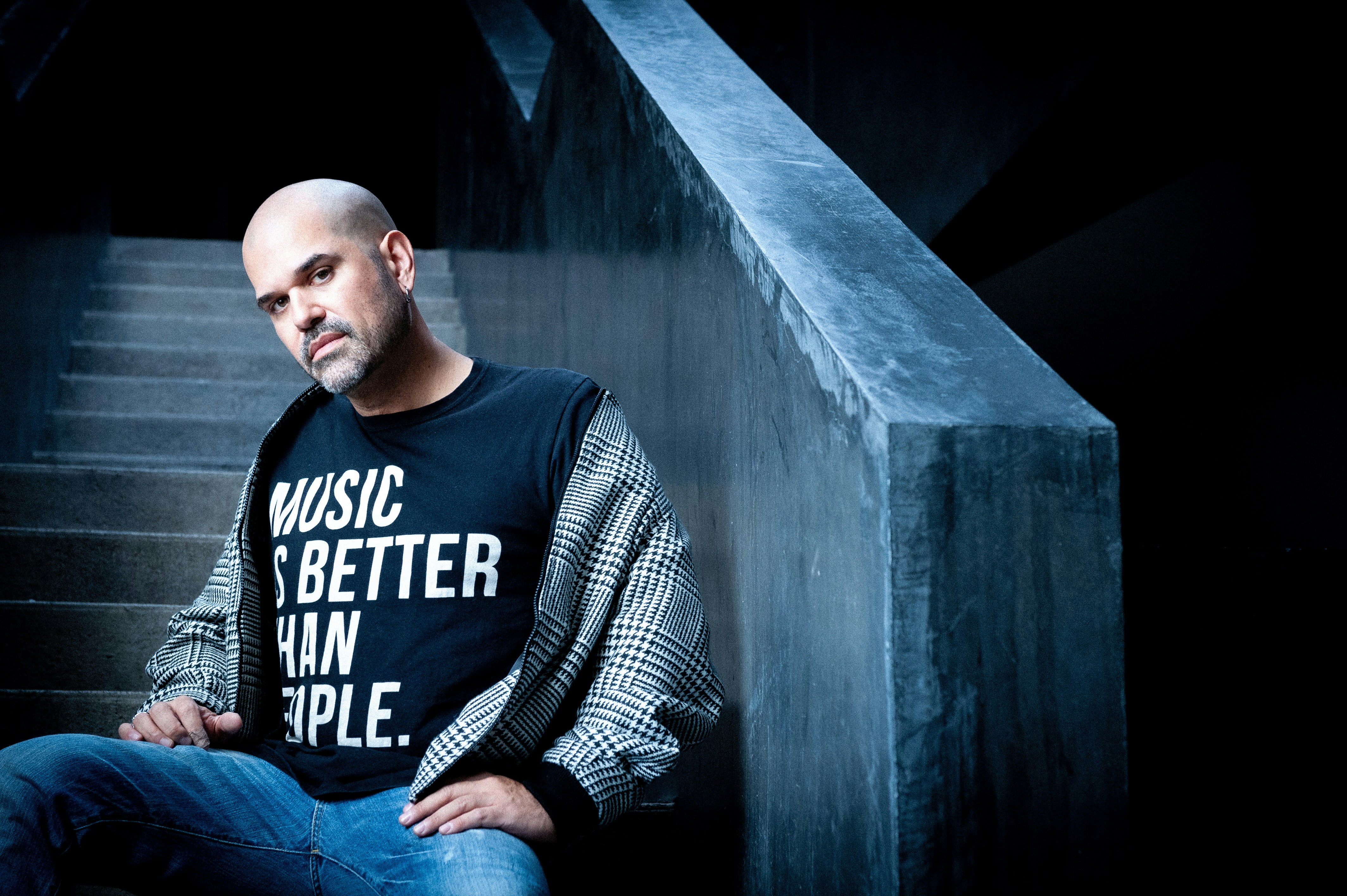 A man sits on a staircase, wearing a shirt that boldly declares 'MUSIC IS BETTER THAN PIMPLE.' The interplay of light and shadow enhances the scene's depth.