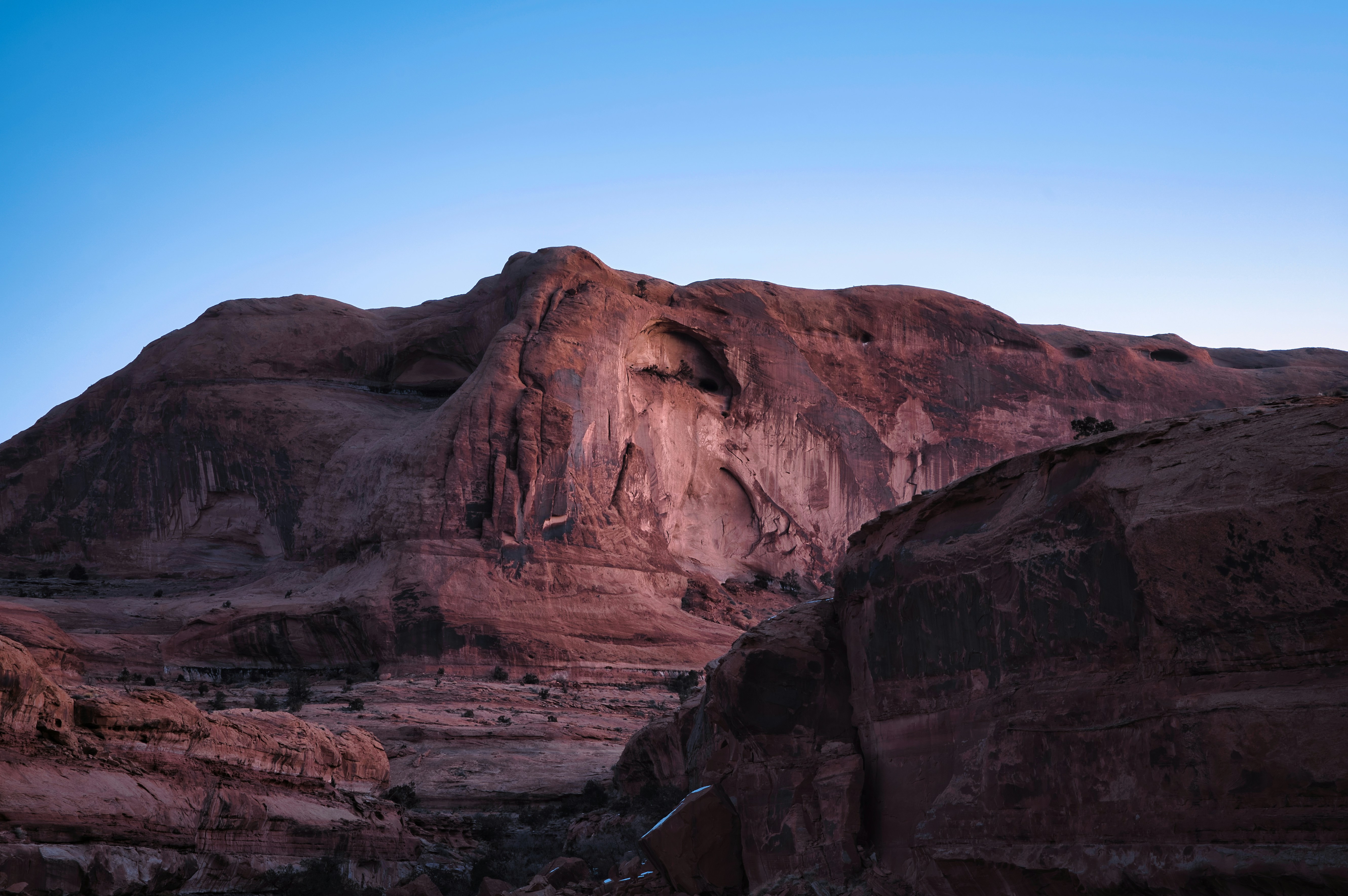 Sunrise light casts shadows on a brown rocky mountain under a clear blue sky.