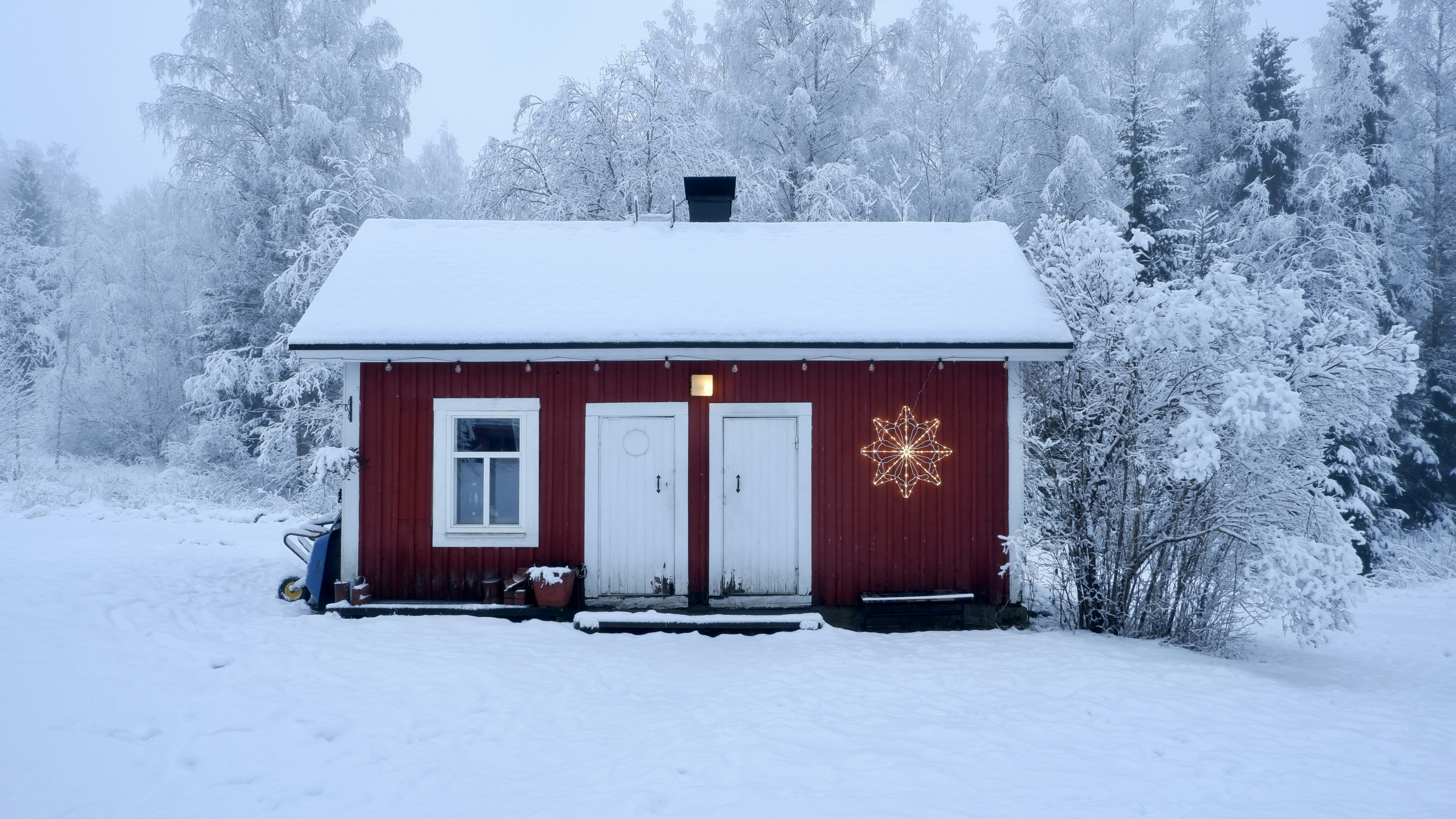 Charming red cabin adorned with a snowflake decoration surrounded by a winter wonderland of frosted trees and soft snow.
