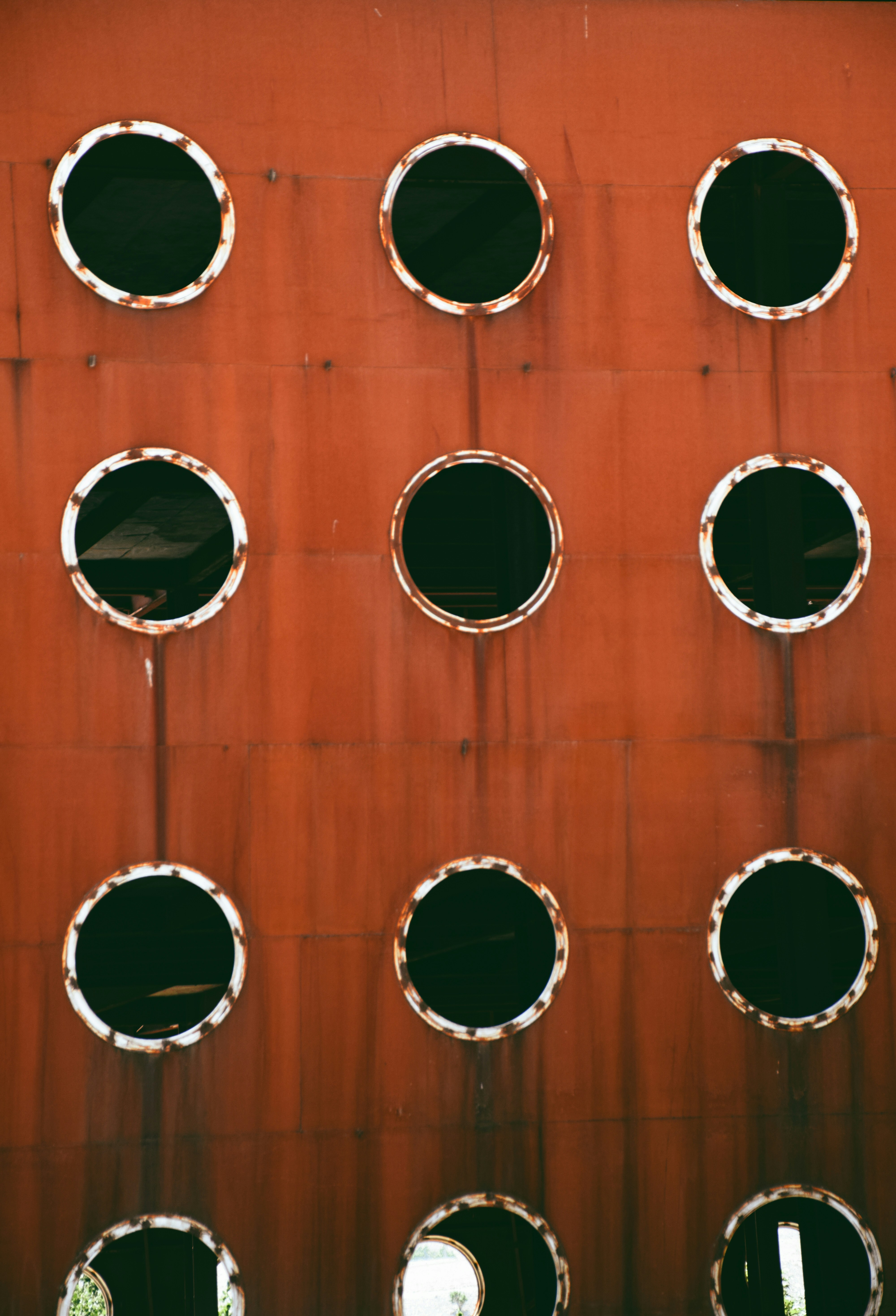Nine Circular Windows in a Rusted Red Panel: Geometry in Weathered Steel