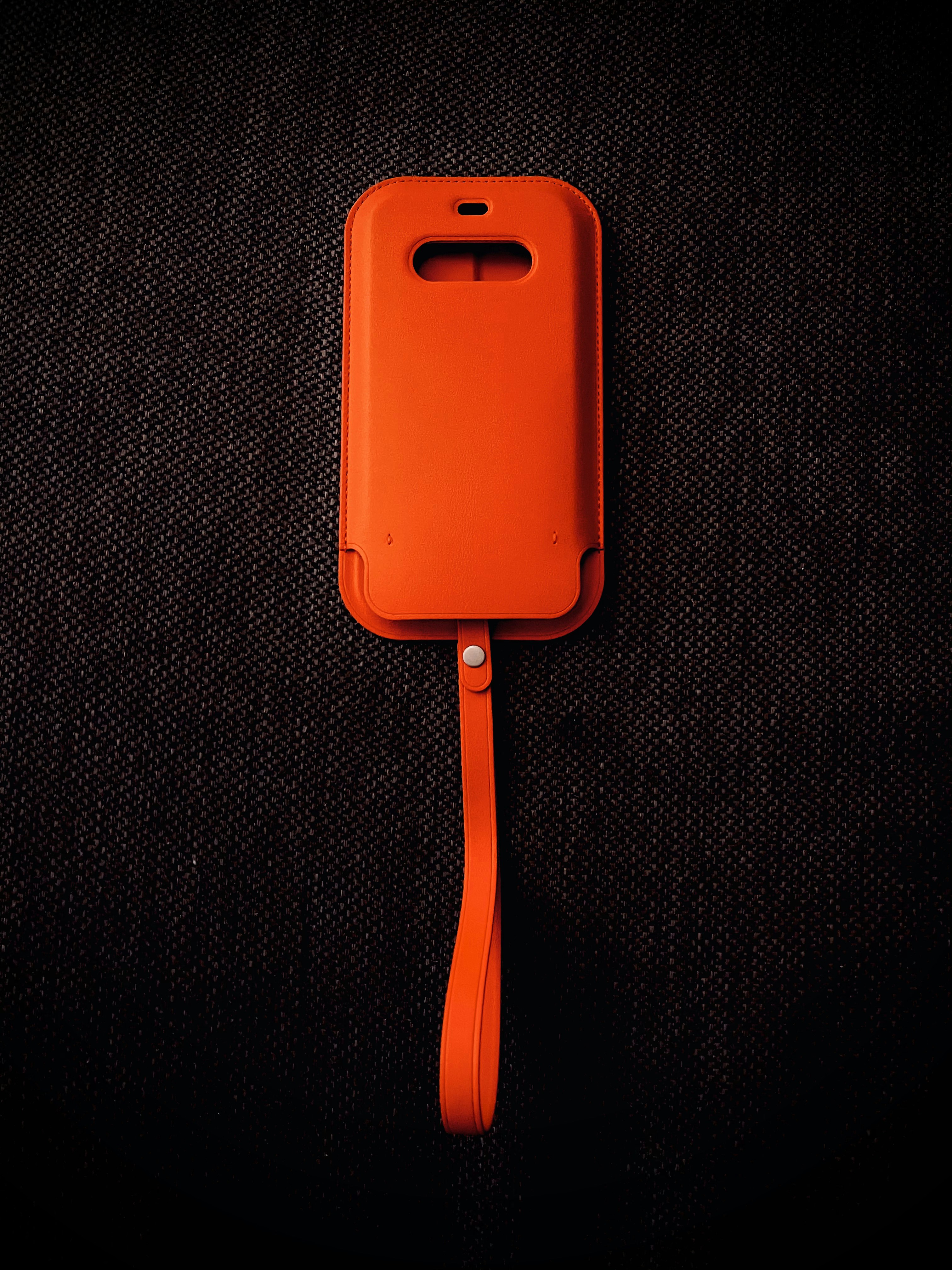 Orange smartphone case resting on a textured black surface, highlighting its sleek design and functionality.
