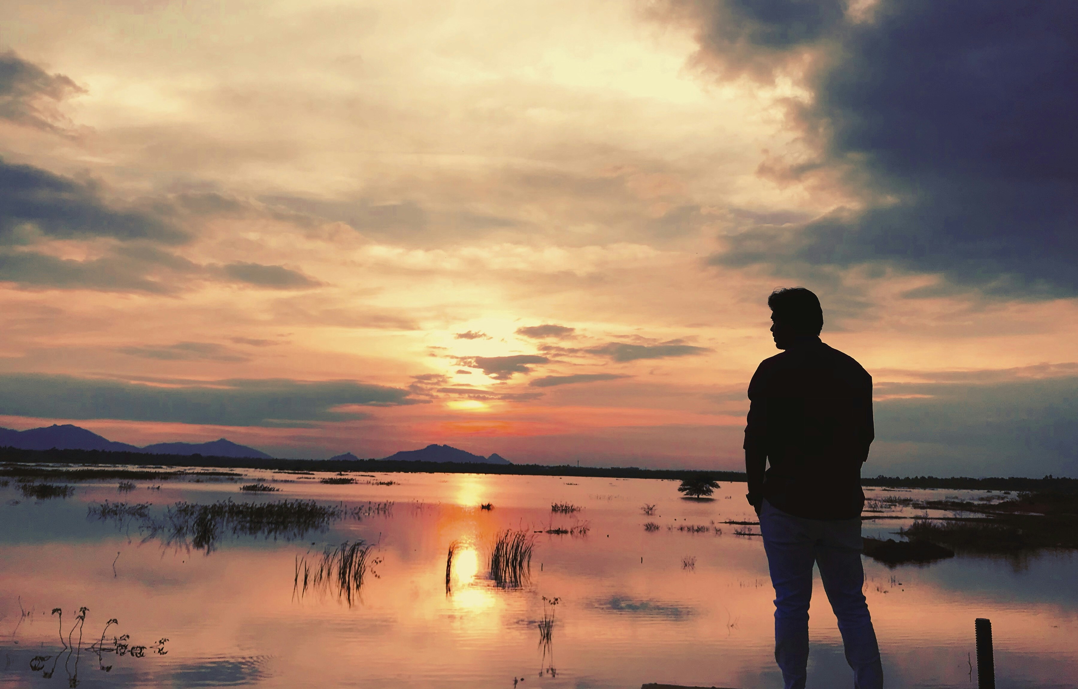 Silhouette of a person standing by a tranquil lake at sunset, with vibrant colors reflecting on the water's surface.