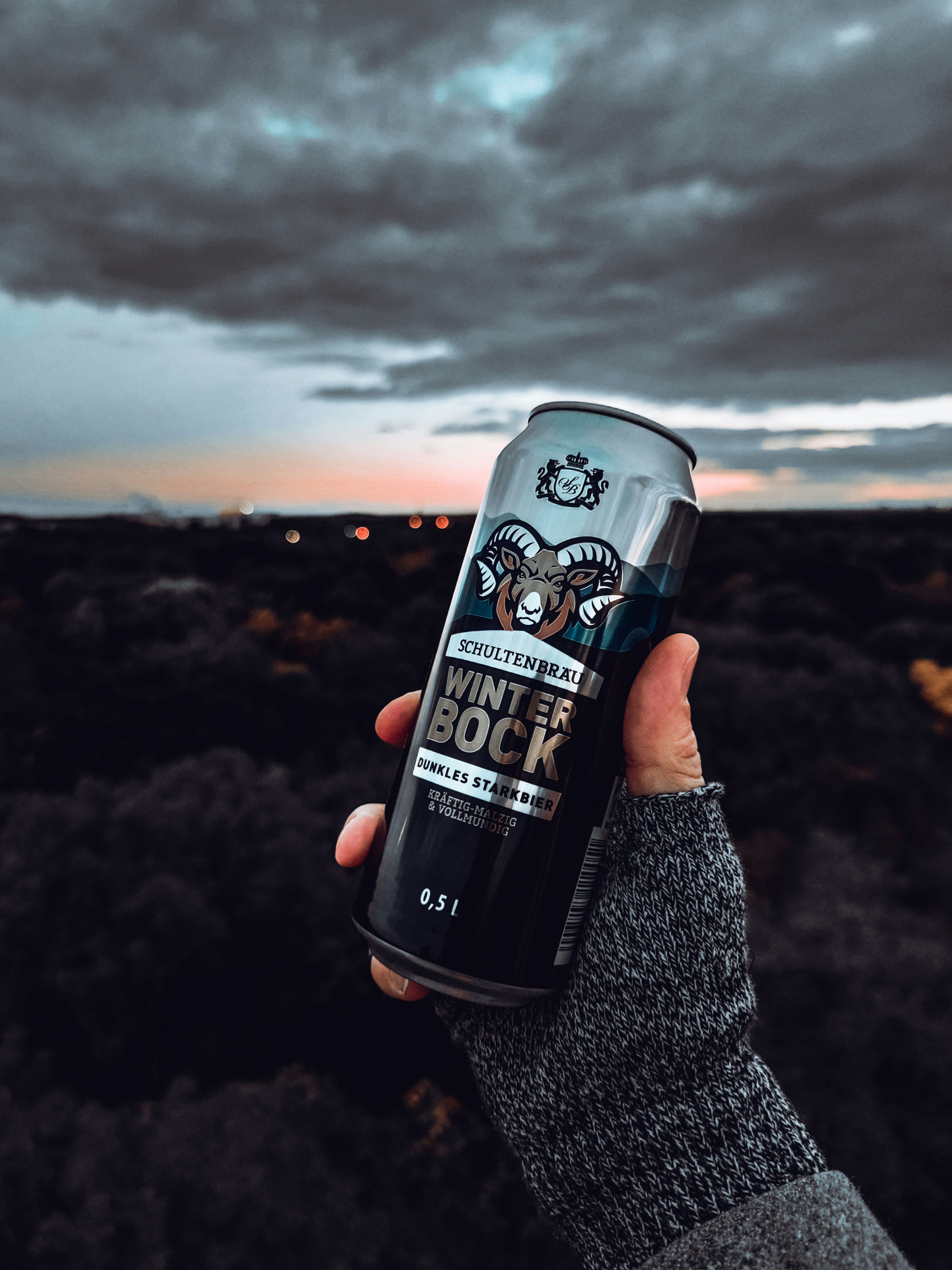 Hand holding a can of Schultenbrau Winter Bock against a twilight sky, showcasing the blend of nature and leisure.