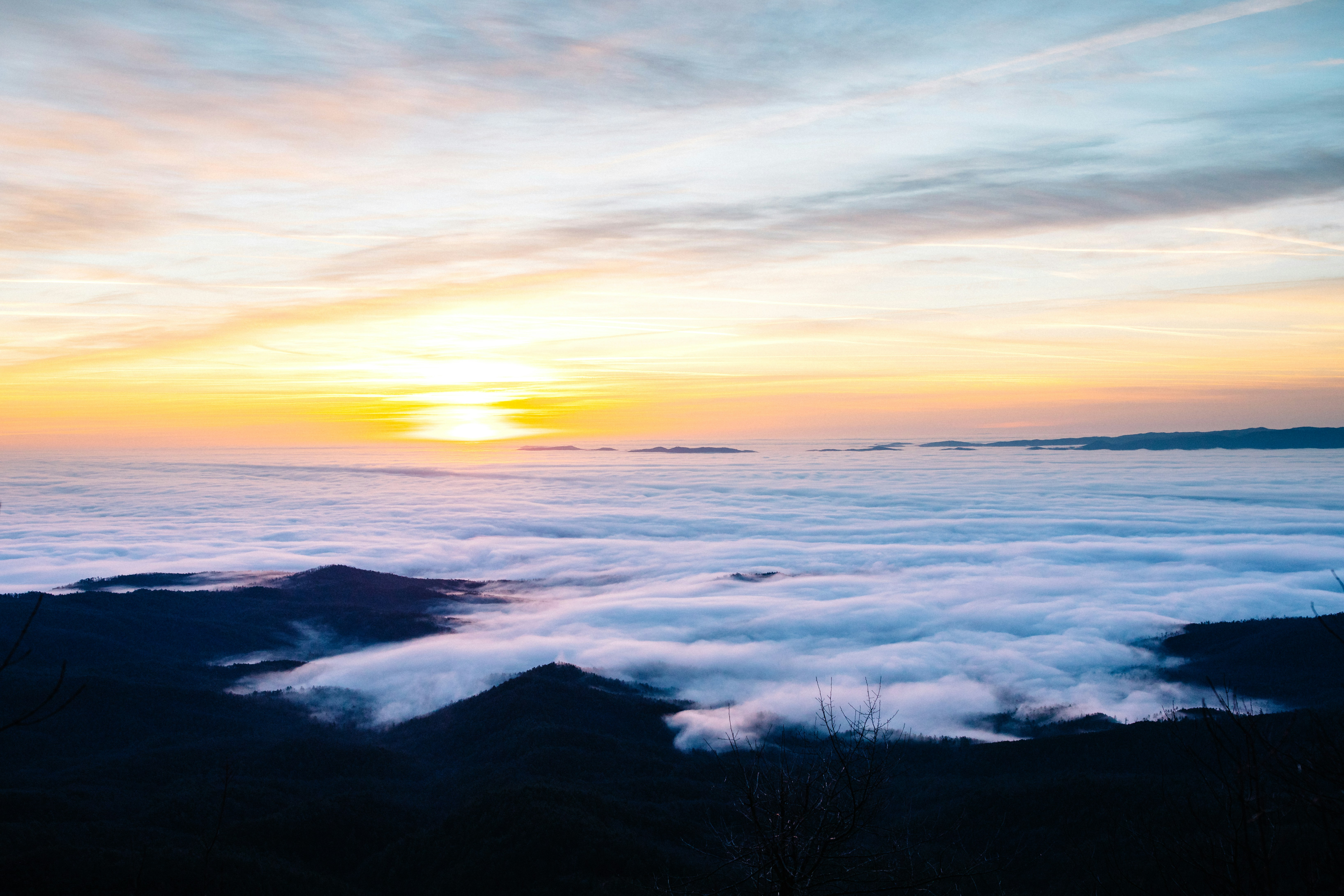 Golden sunrise illuminating a vast sea of clouds over dark mountain silhouettes.