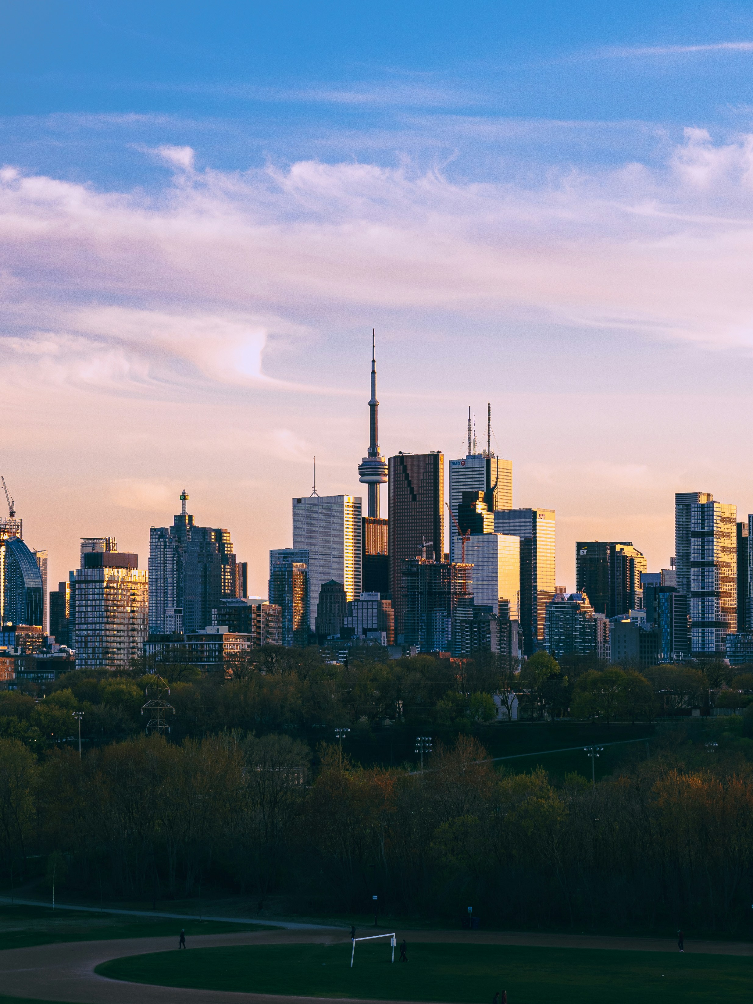 City skyline illuminated by the soft hues of dusk, featuring prominent skyscrapers and the CN Tower. The scene captures the essence of urban life transitioning into evening.