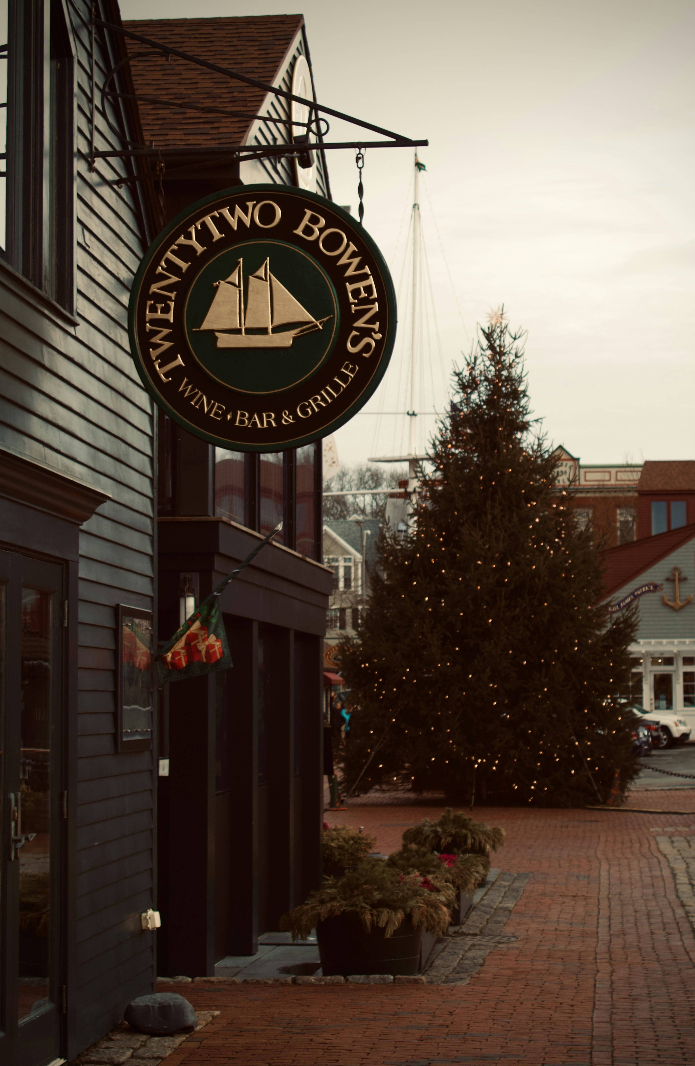 Restaurant sign at the wharf with holiday lights on a nearby tree under an overcast sky.