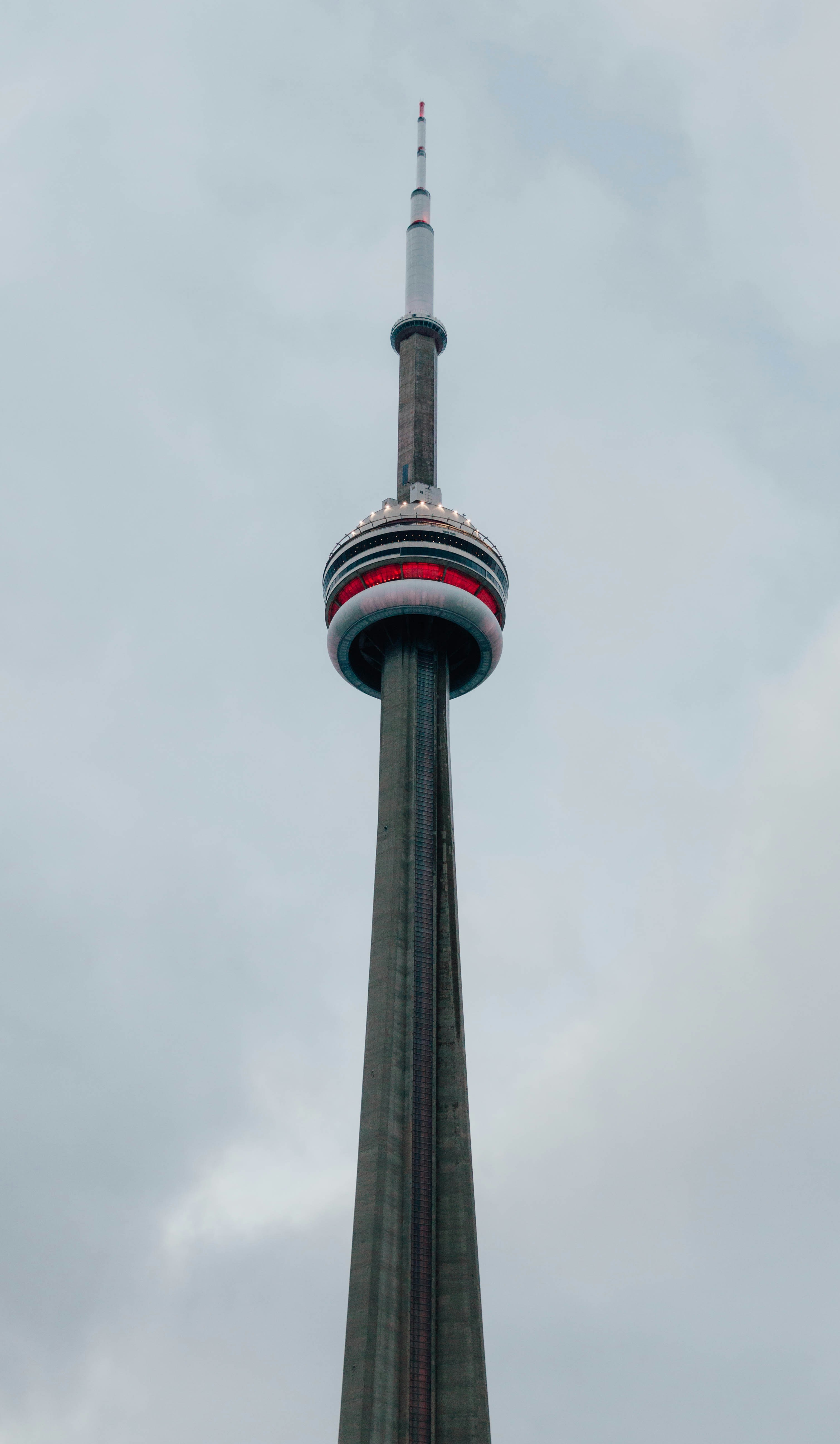 Tall gray tower reaching into a cloudy sky with red accents encircling its midsection.