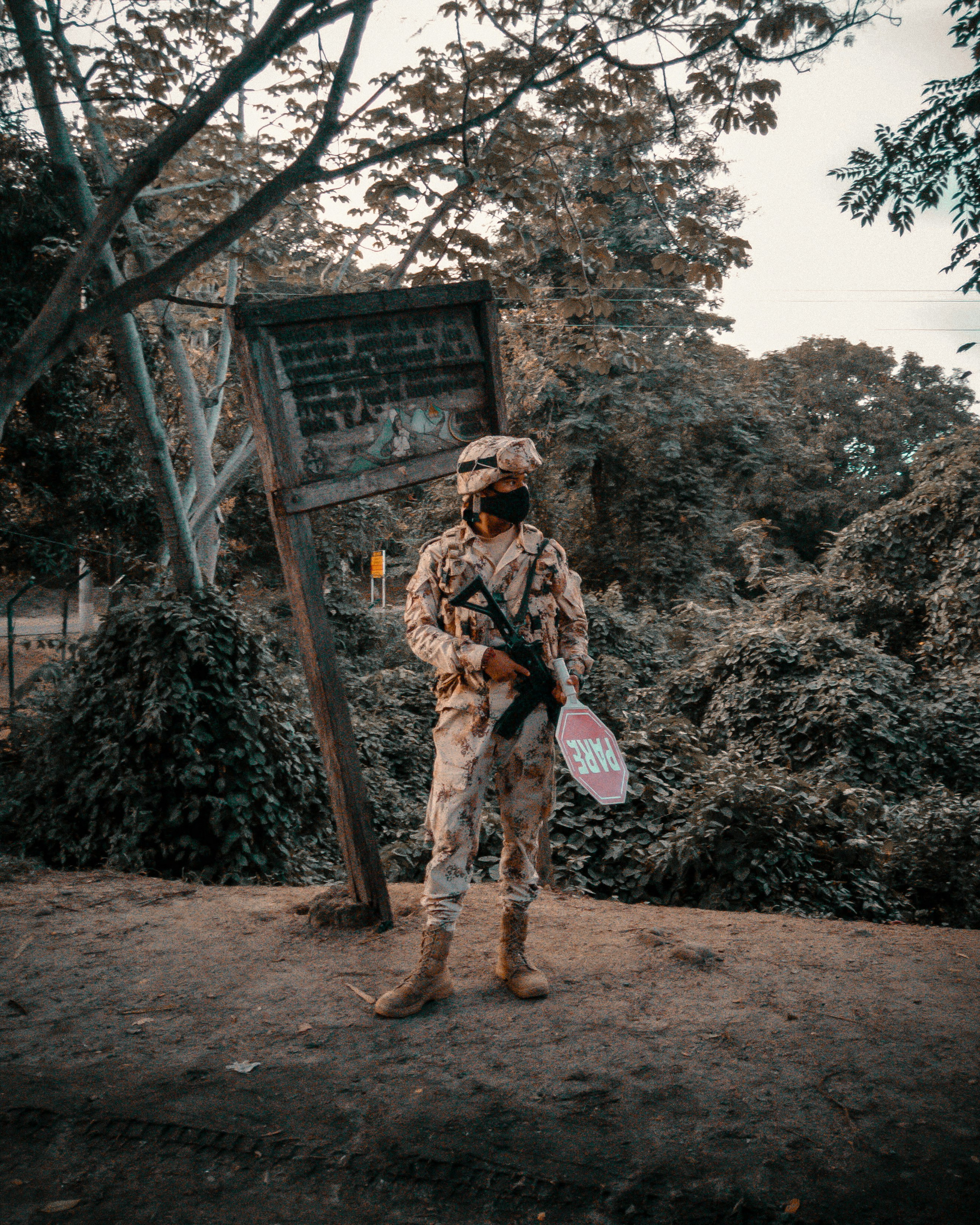 Soldier at a cautionary treeline: a lone figure with a stop sign