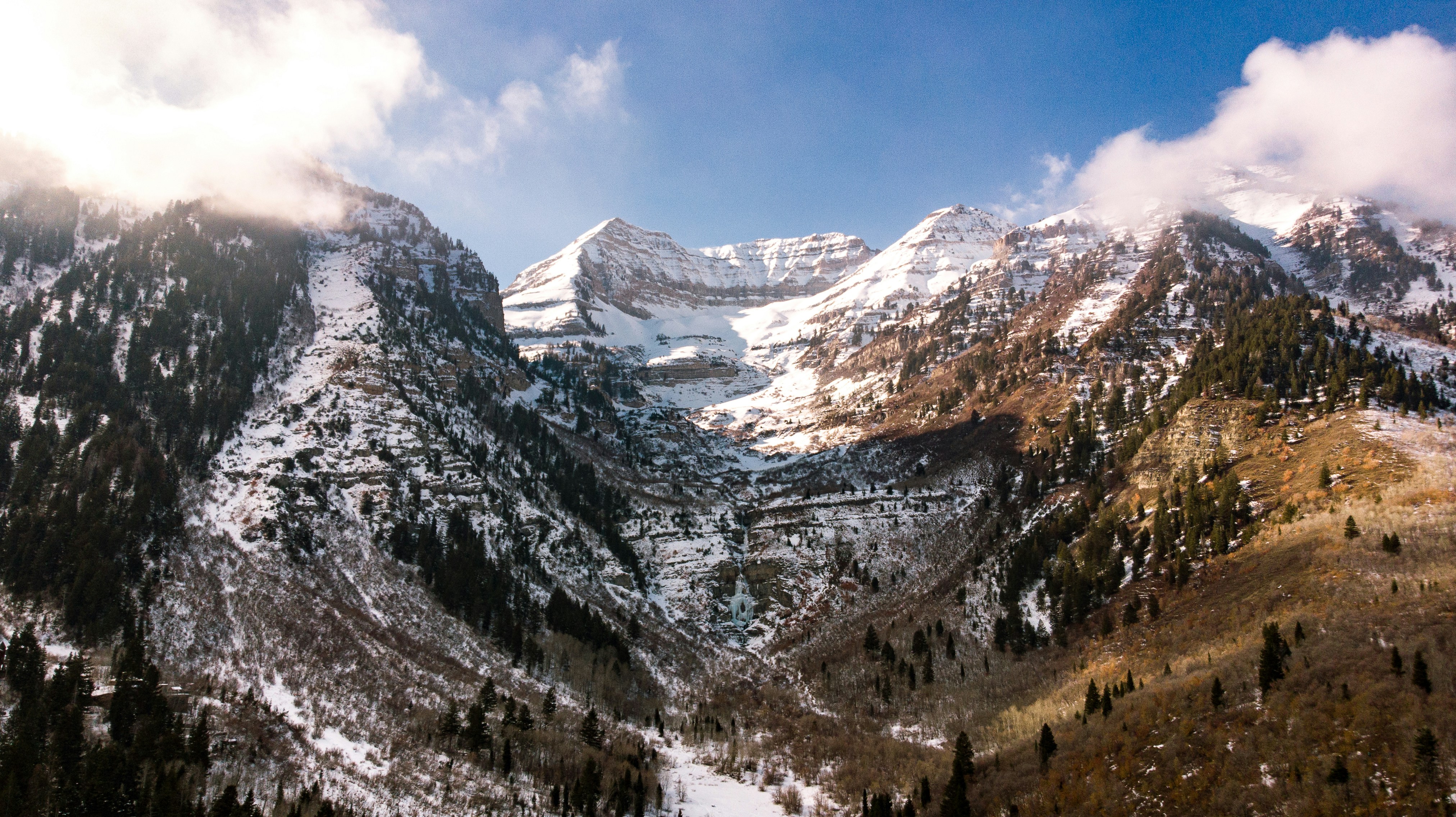 Snow-dusted mountains rise majestically beneath a clear blue sky, with scattered clouds adding depth to the scene.