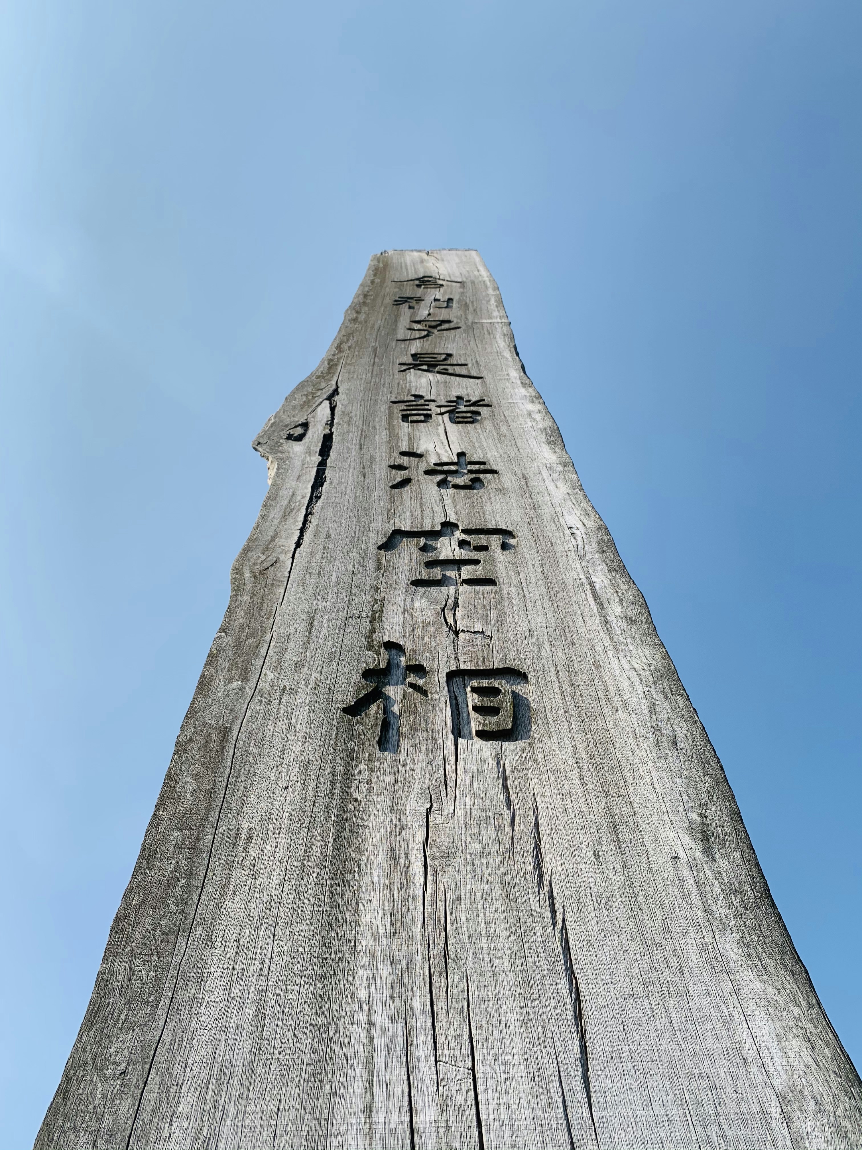 Vertical Glyphs on a Weathered Timber Spire Against a Clear Azure Sky