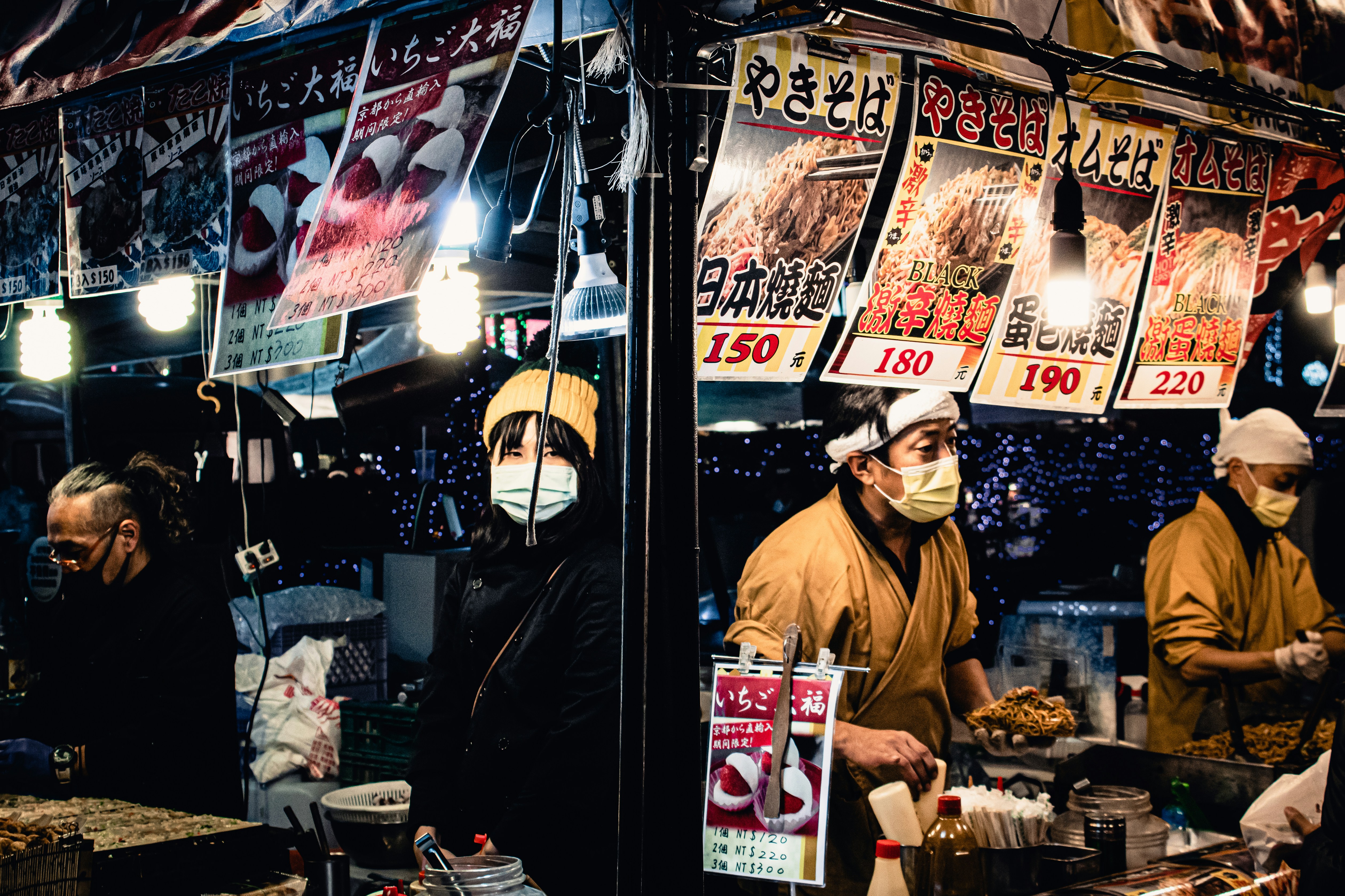 Vibrant street food stall bustling with vendors and illuminated menus, showcasing delicious offerings. The scene captures the lively atmosphere of a night market.