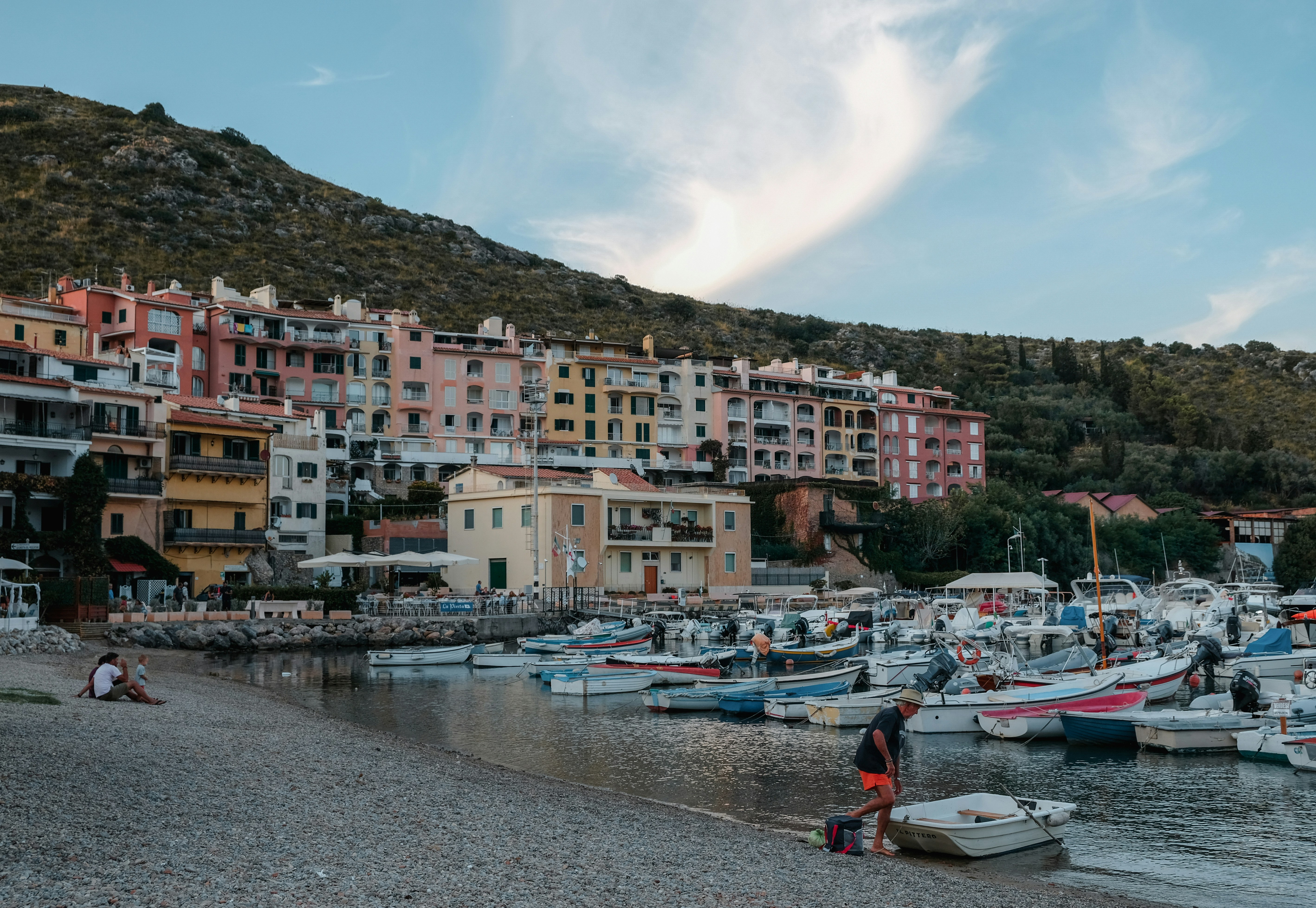 Colorful hillside buildings overlook a tranquil harbor filled with boats under a dramatic sky.