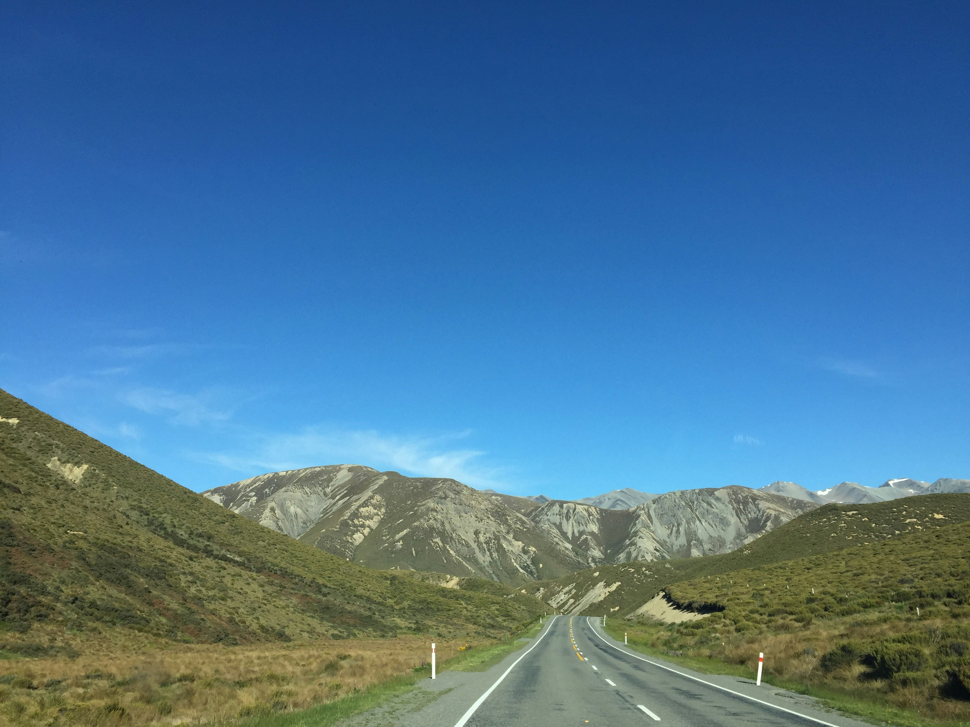 gray asphalt road near green grass field and mountains under blue sky during daytime