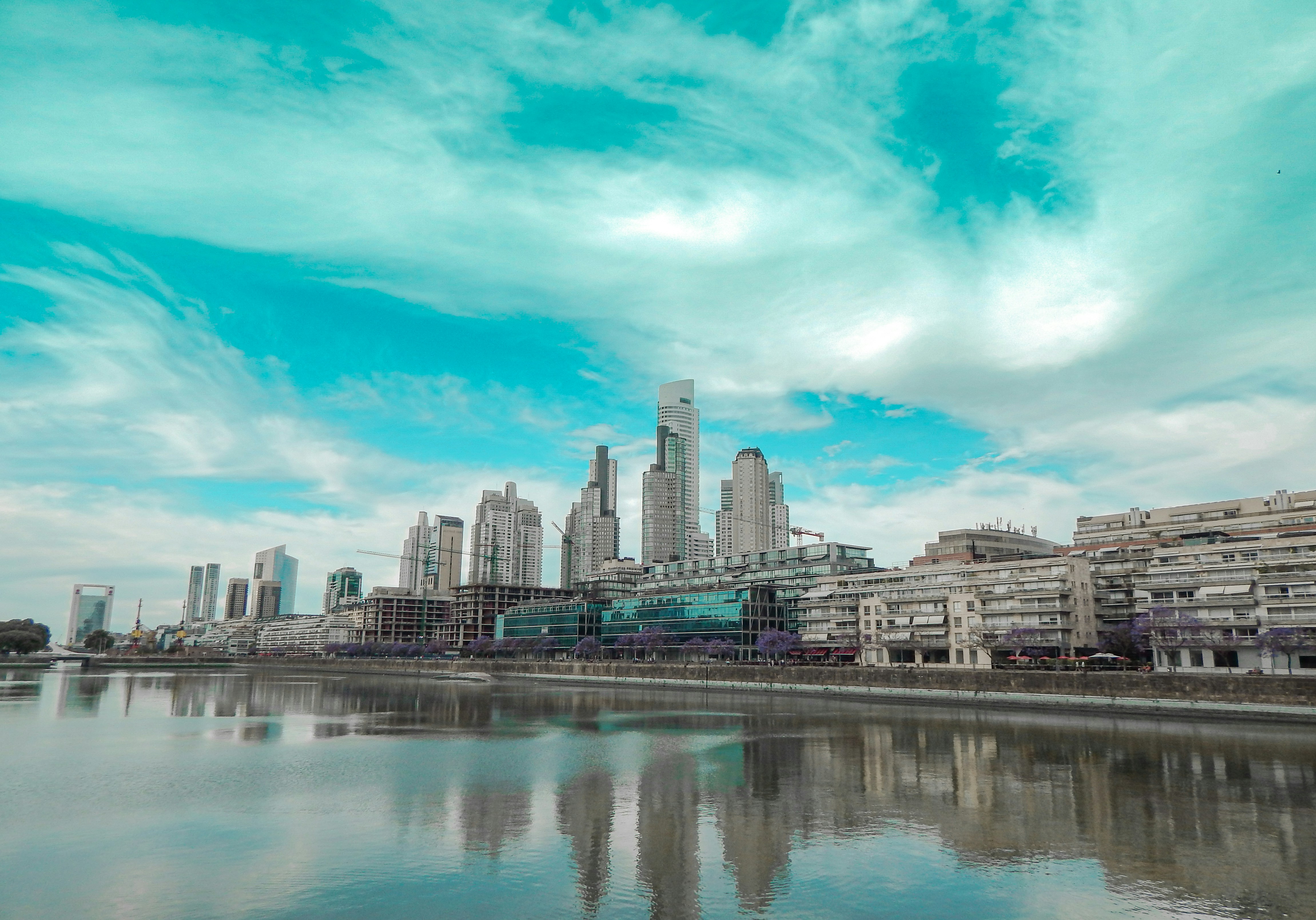 City skyline reflected in calm waters under a vibrant turquoise sky.