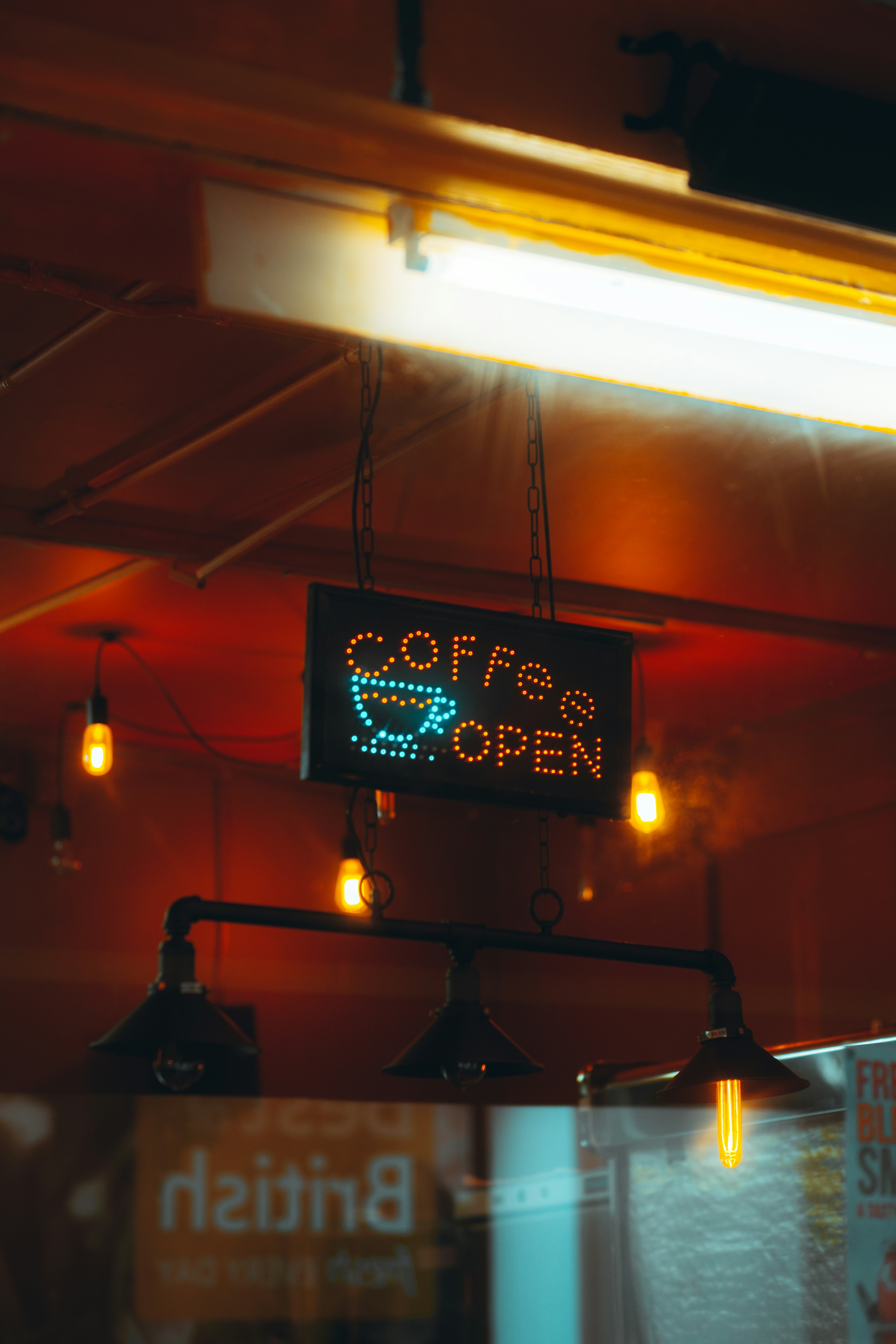 Illuminated 'COFFEE OPEN' sign hanging in a cozy café, surrounded by warm lighting and rustic decor.