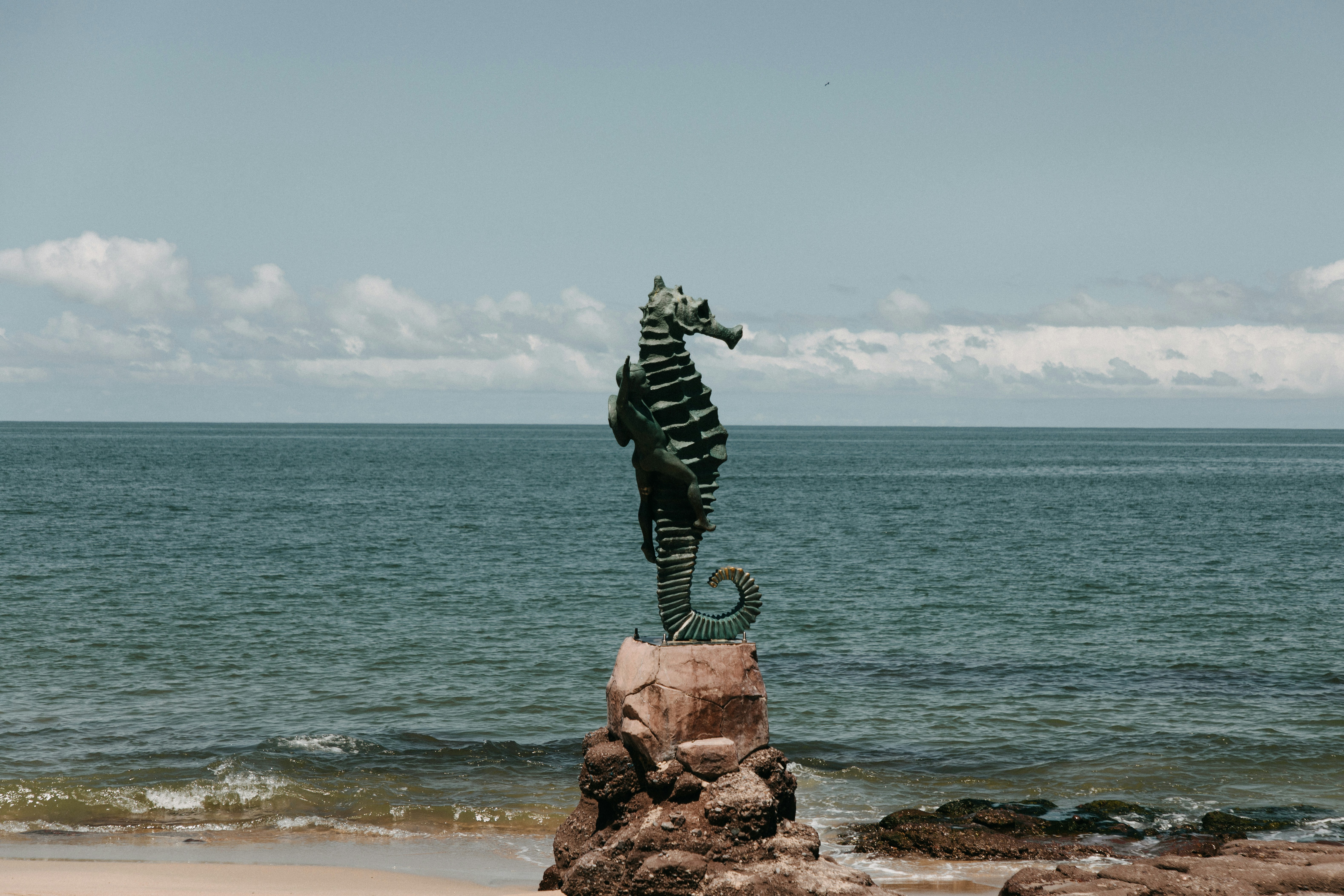 Statue of man on rock formation near sea under blue sky during daytime ...