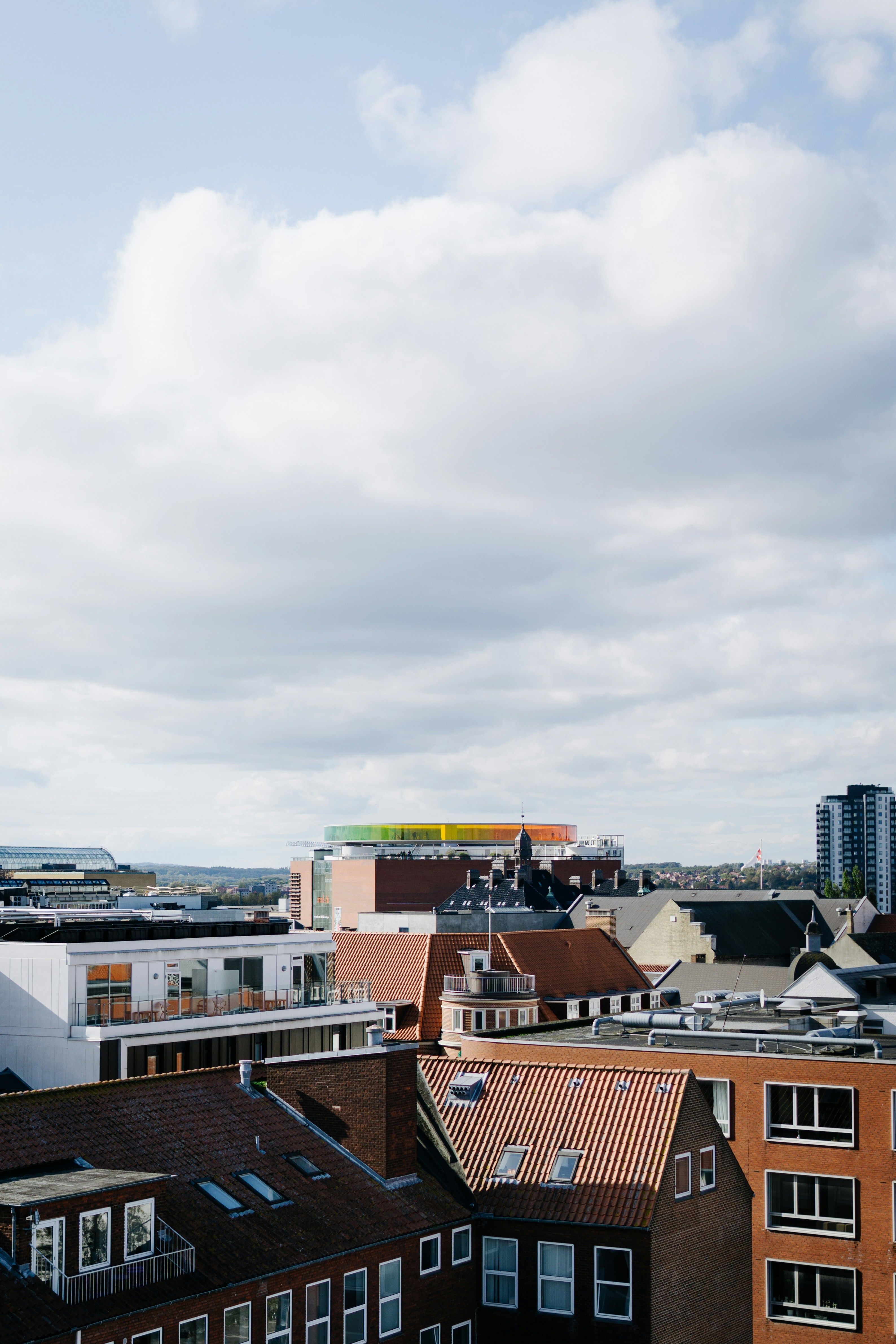 Colorful rooftop structure contrasts with the urban landscape, showcasing modern architecture against a backdrop of clouds.