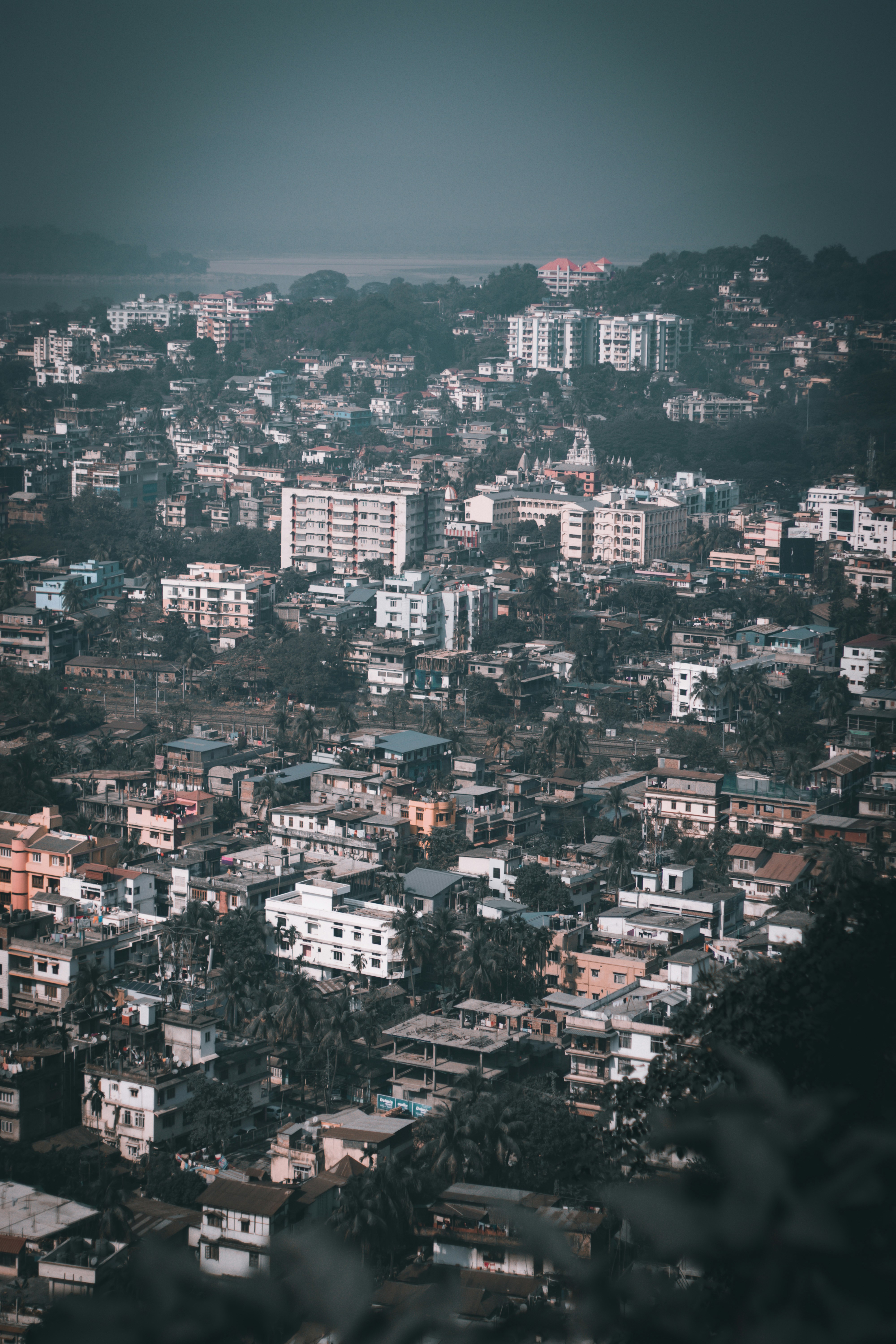 Aerial view of a densely populated urban area featuring a mix of residential and commercial buildings amidst lush greenery. The scene captures the intricate layout of the city.