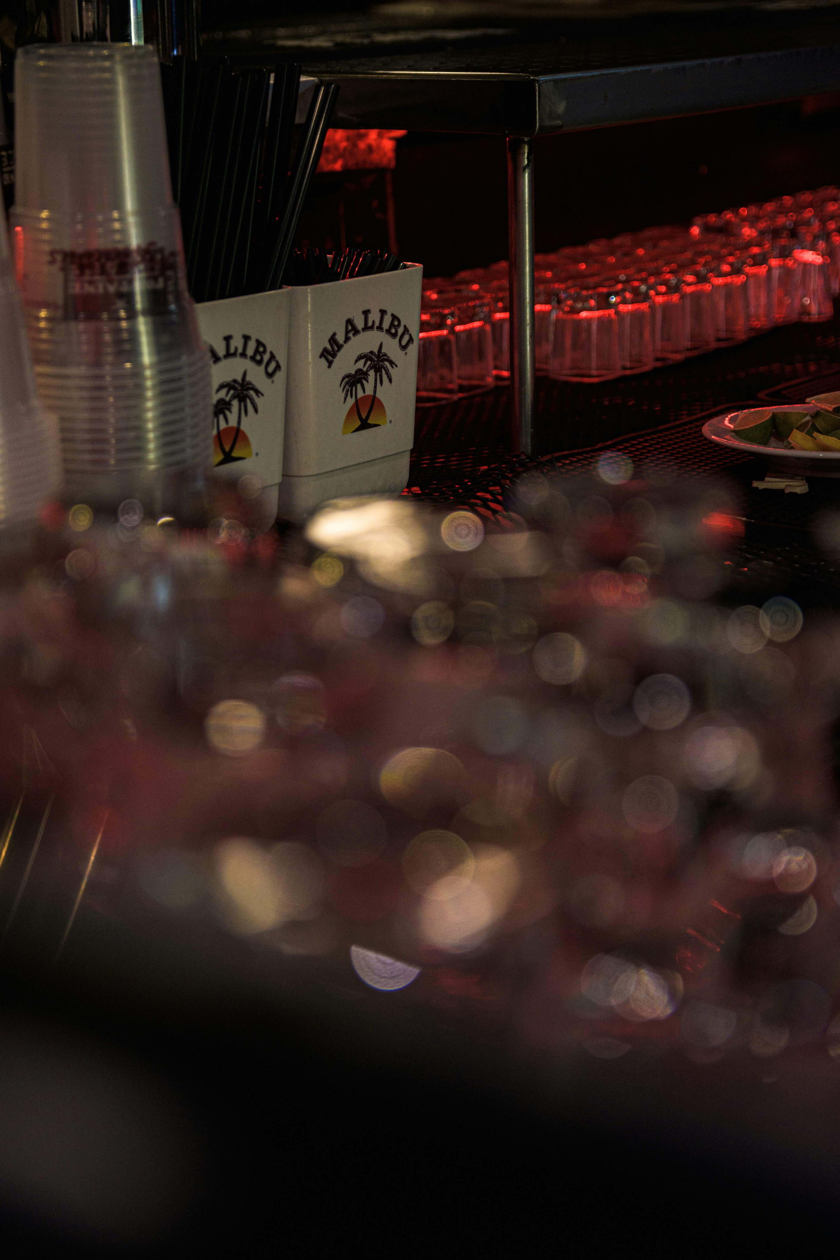 Bar scene featuring Malibu cups and illuminated glasses, creating a vibrant atmosphere. The blurred foreground adds depth to the composition.