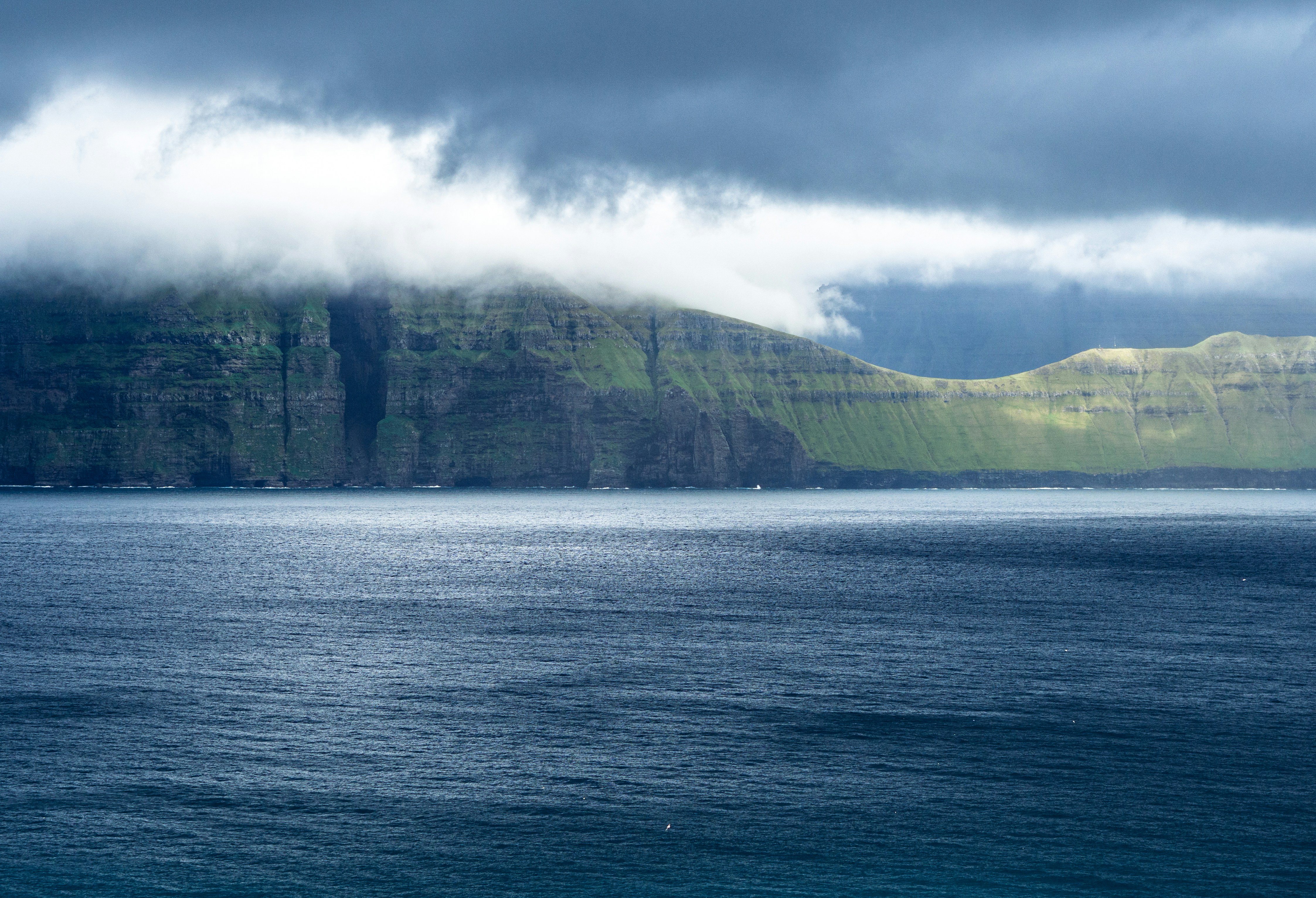 Clouds hover low over rugged green cliffs beside a vast blue ocean.