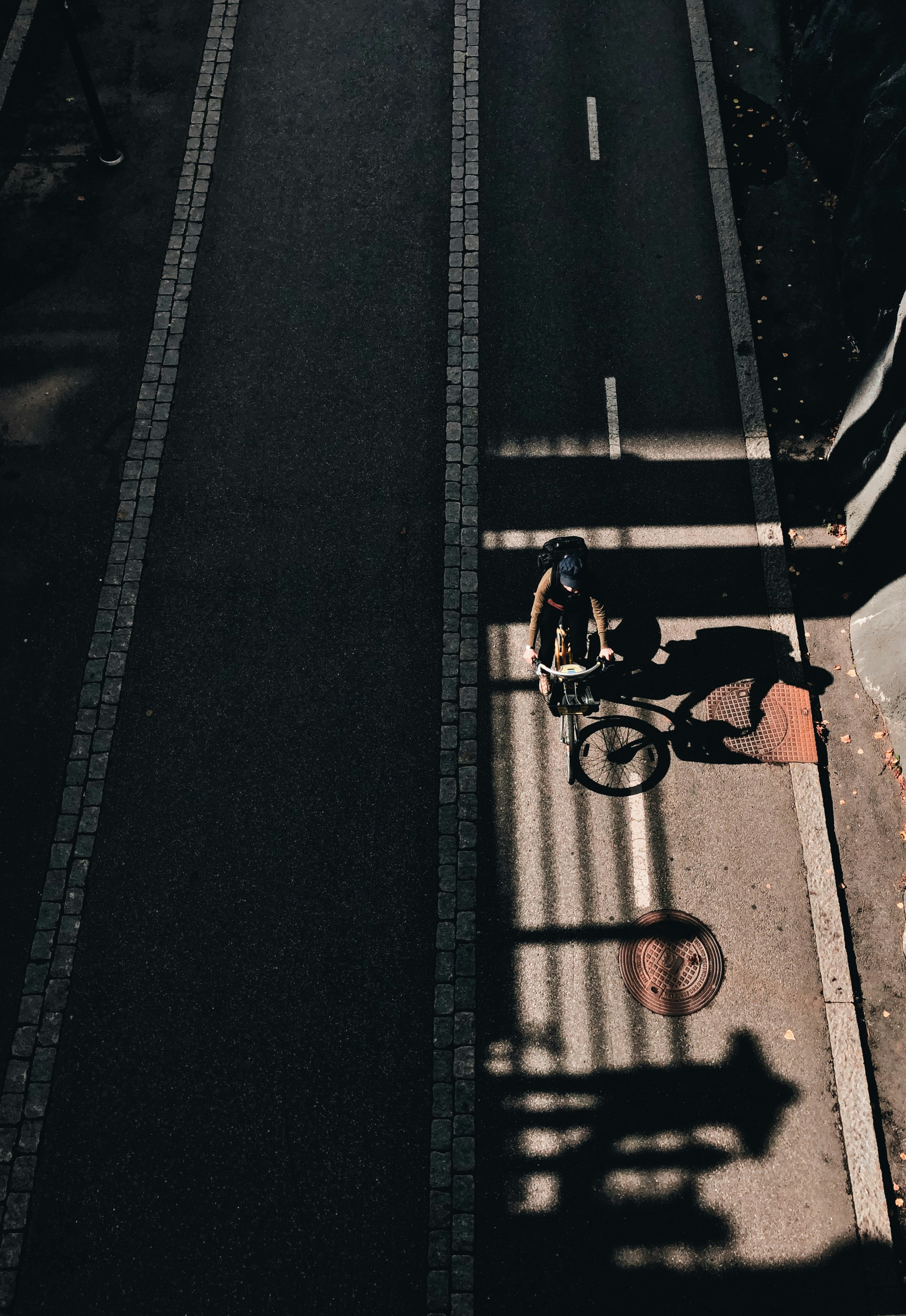 A cyclist navigates a sunlit path, creating dynamic shadows on the asphalt. The interplay of light and shadow adds depth to the urban landscape.