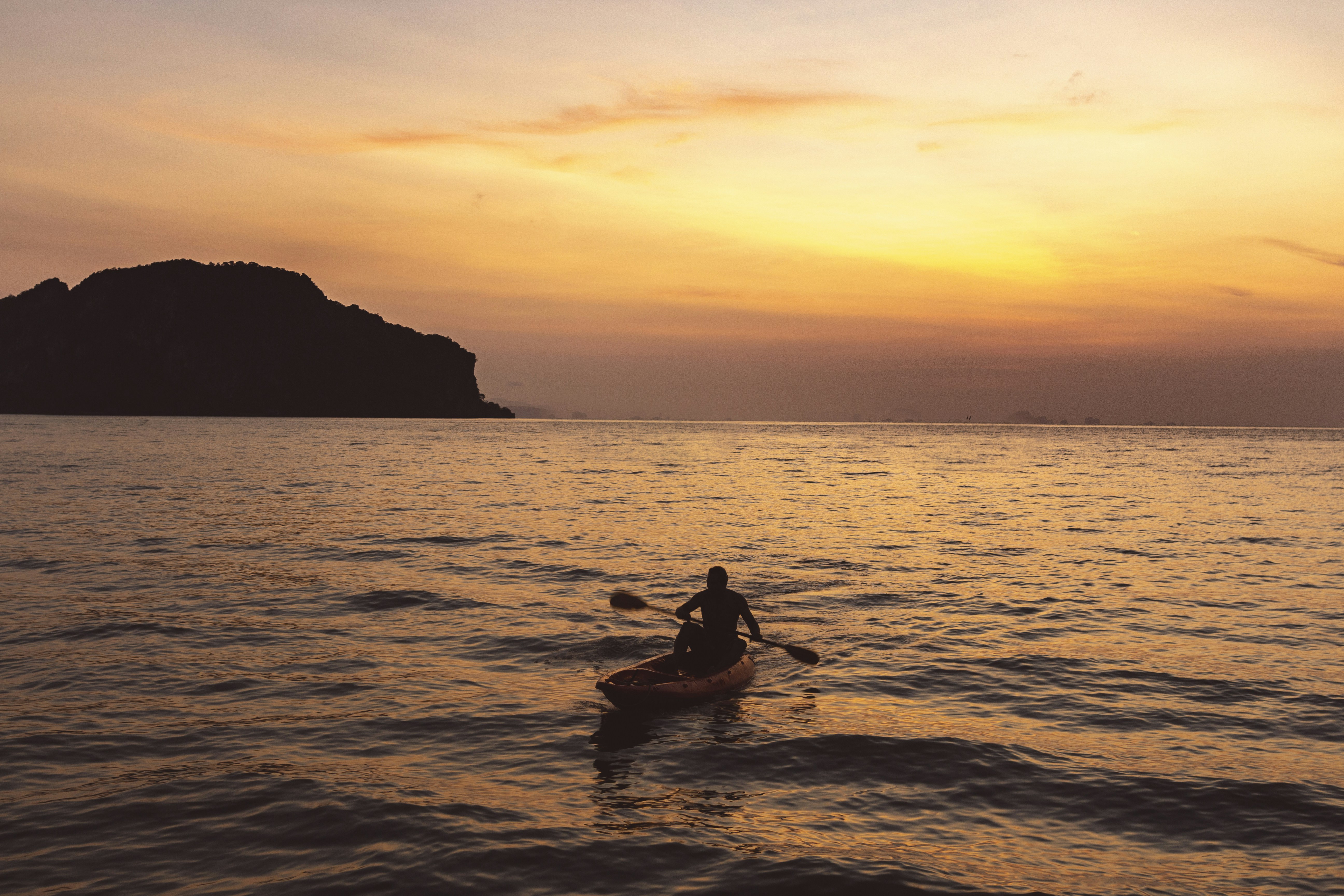 Silhouette of a person paddling a kayak on the ocean at sunset.
